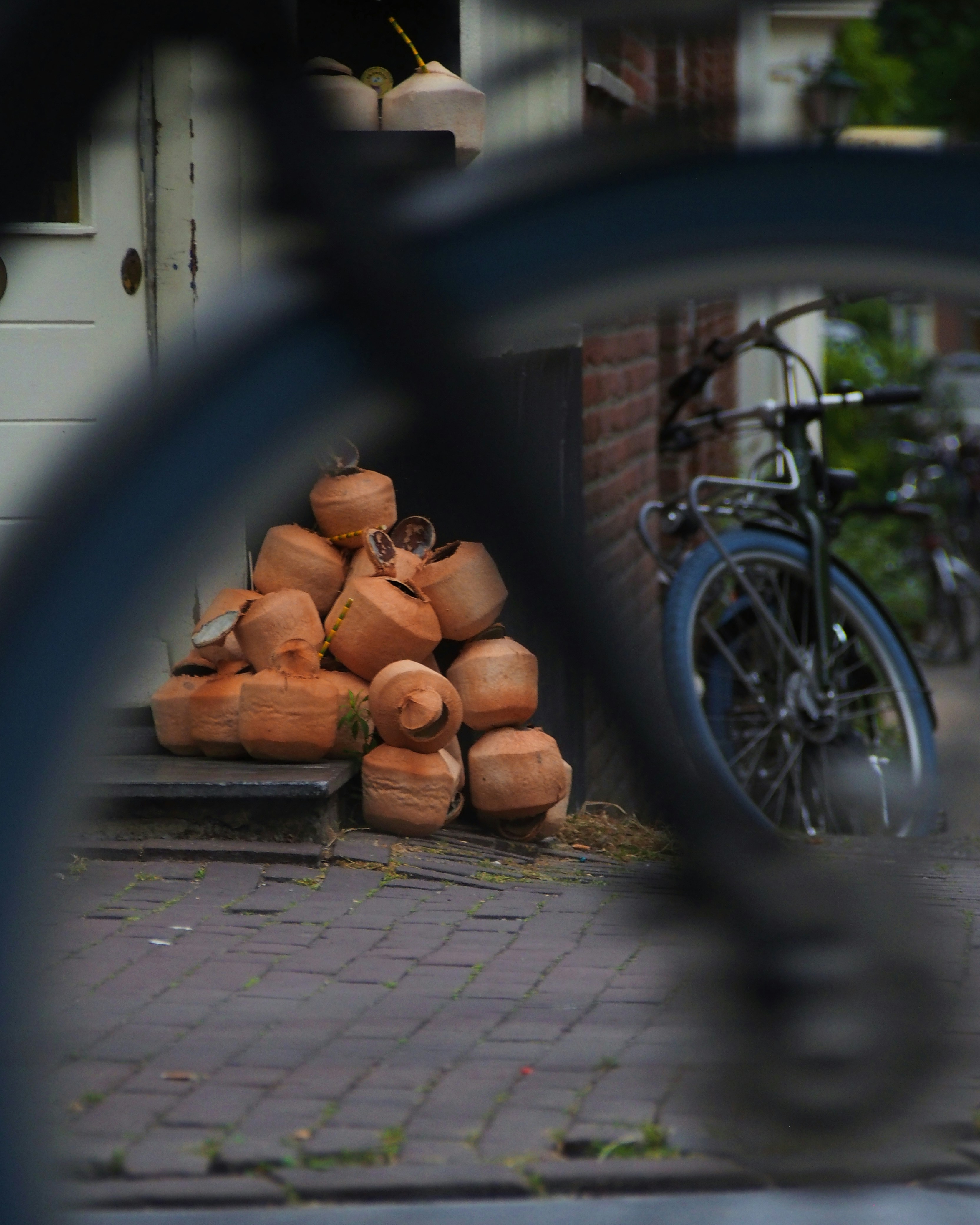 Stacked terracotta pots sit on a doorstep, framed by a passing bicycle wheel and brick wall.