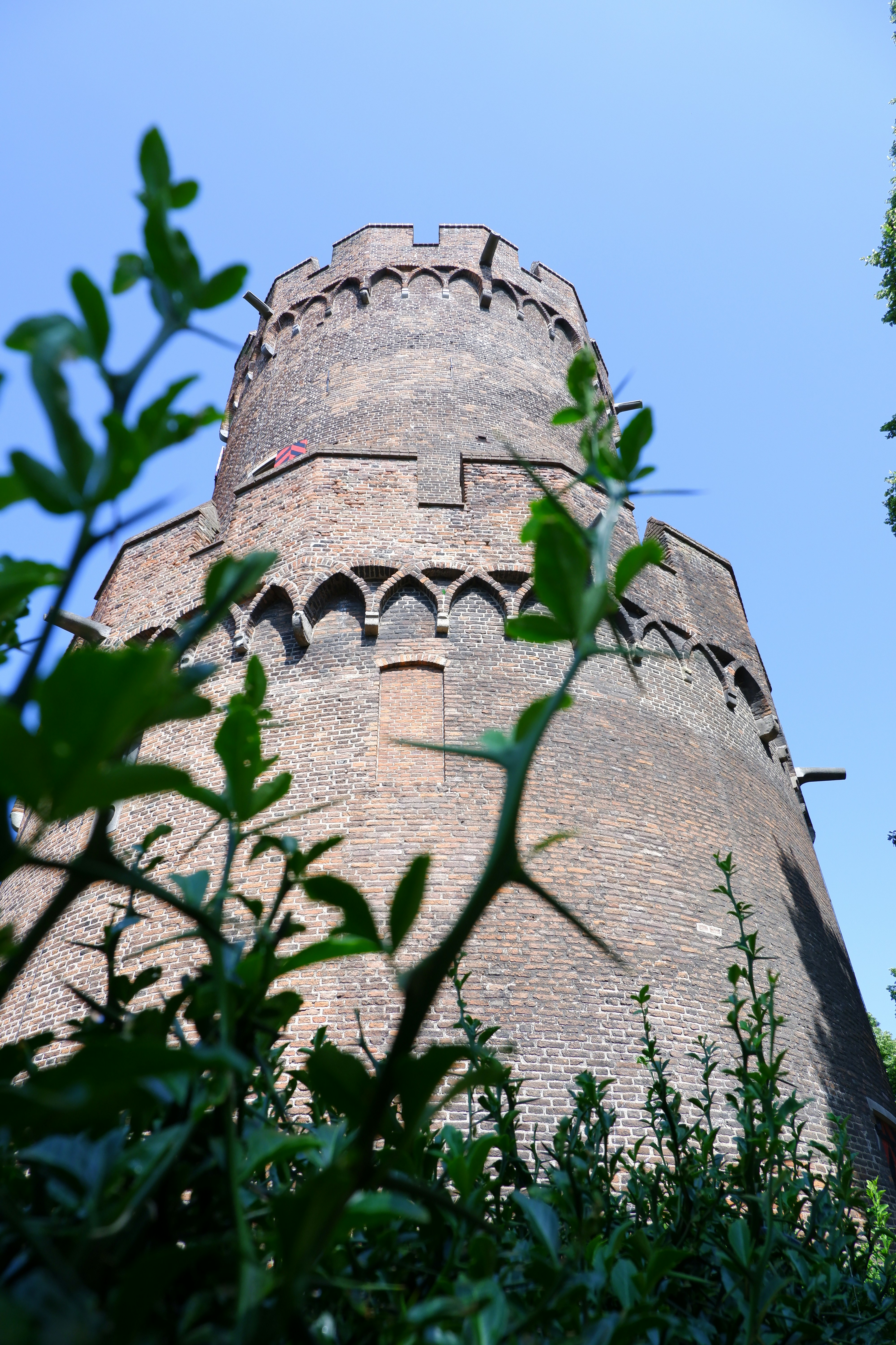 Crenellated Sentinel: Brick Tower Framed by Greenery Under a Blue Sky