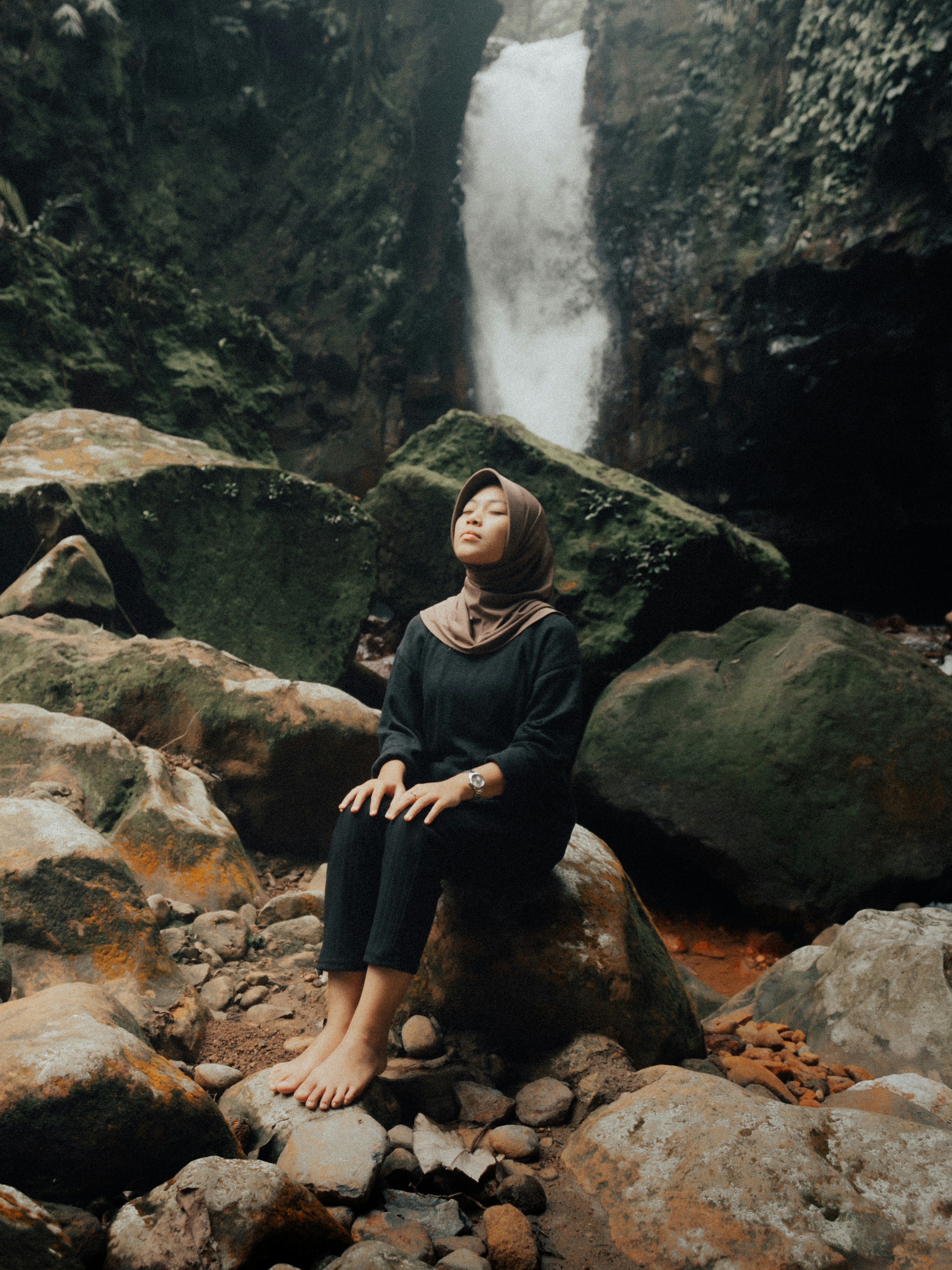 a woman sitting on rocks in front of a waterfall