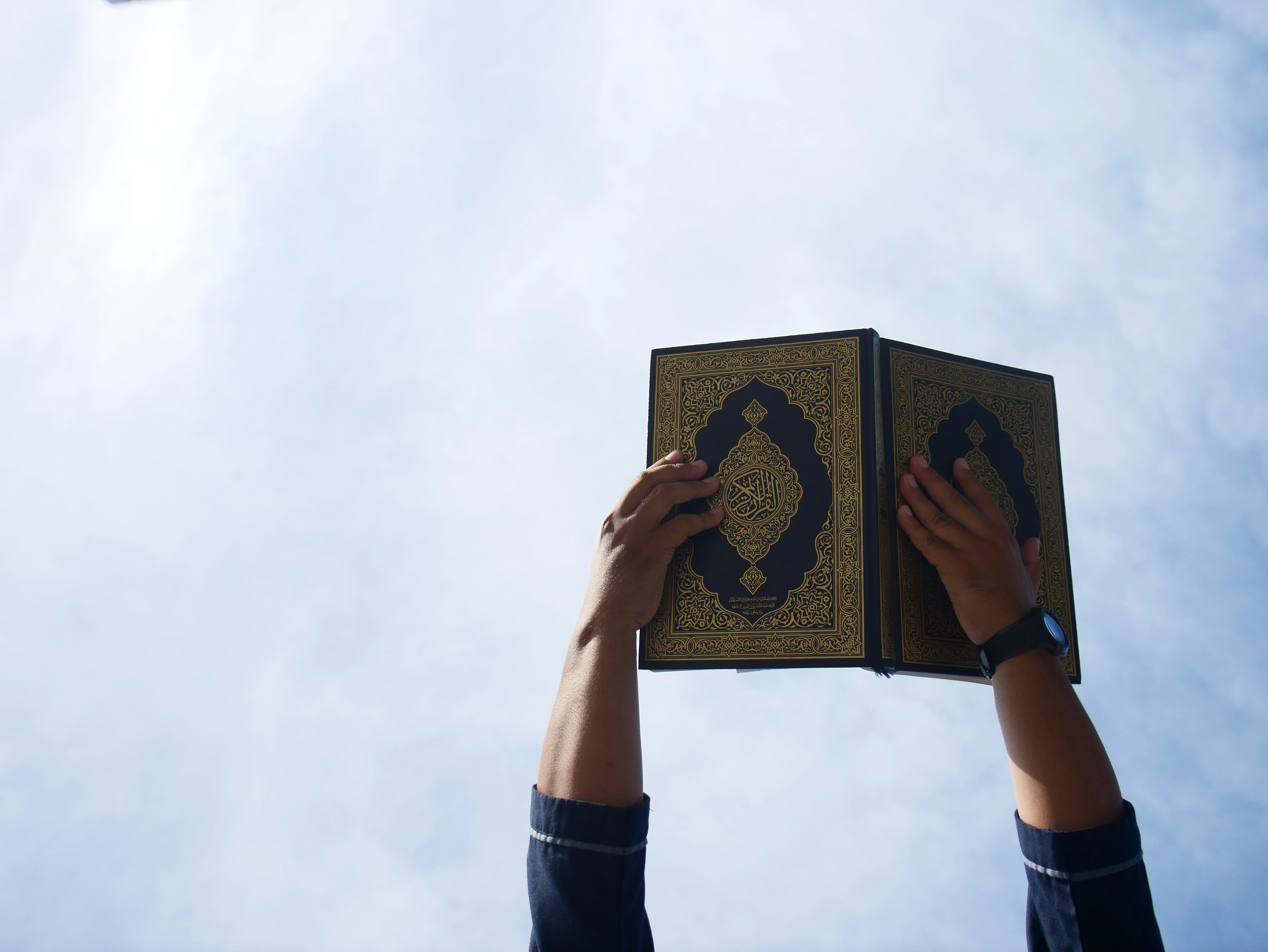Skybound Tome: An Open, Gold-Embossed Scripture Against a Bright Sky