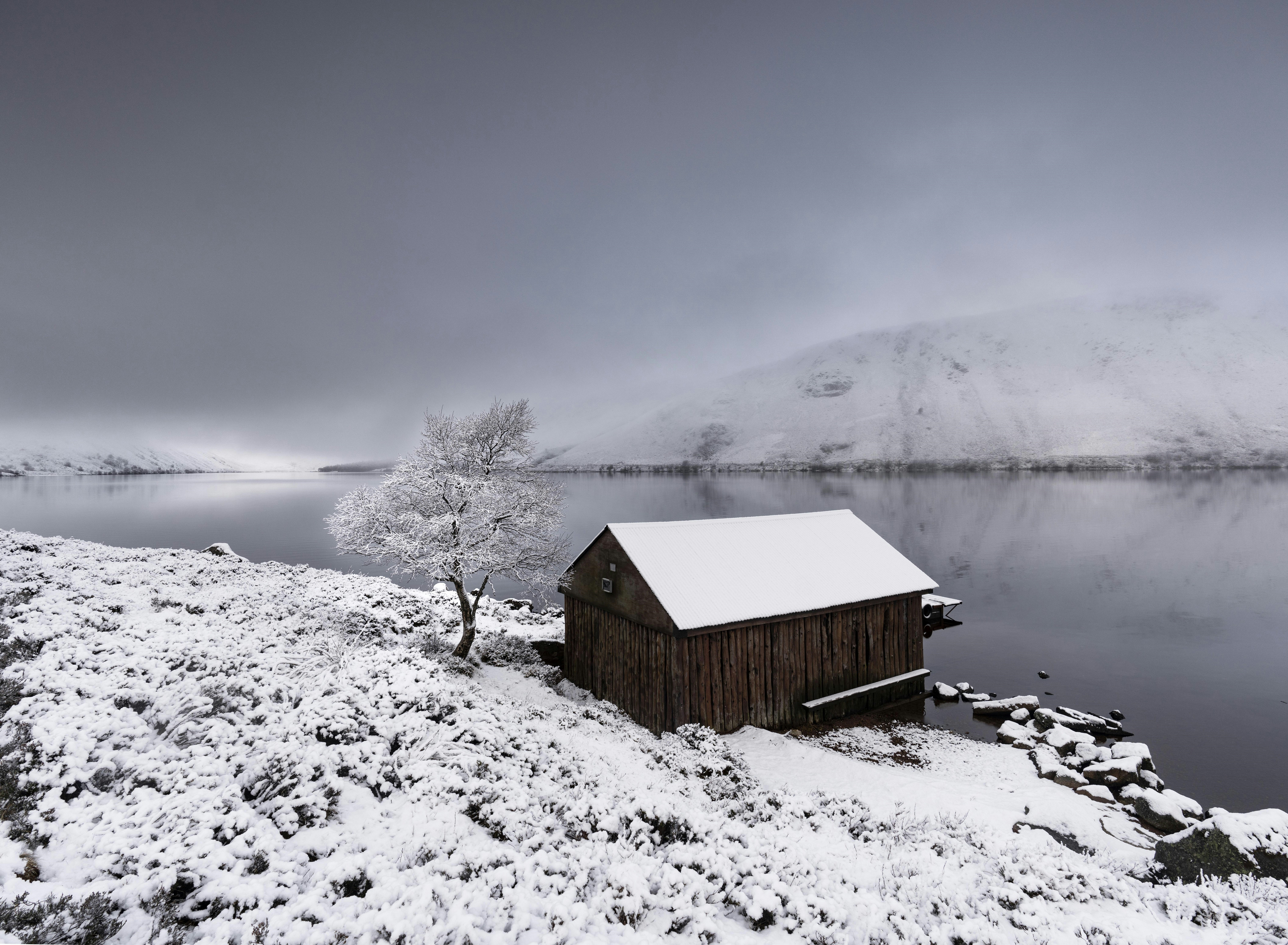 A small cabin on the shore of a lake covered in snow photo – Free Loch ...