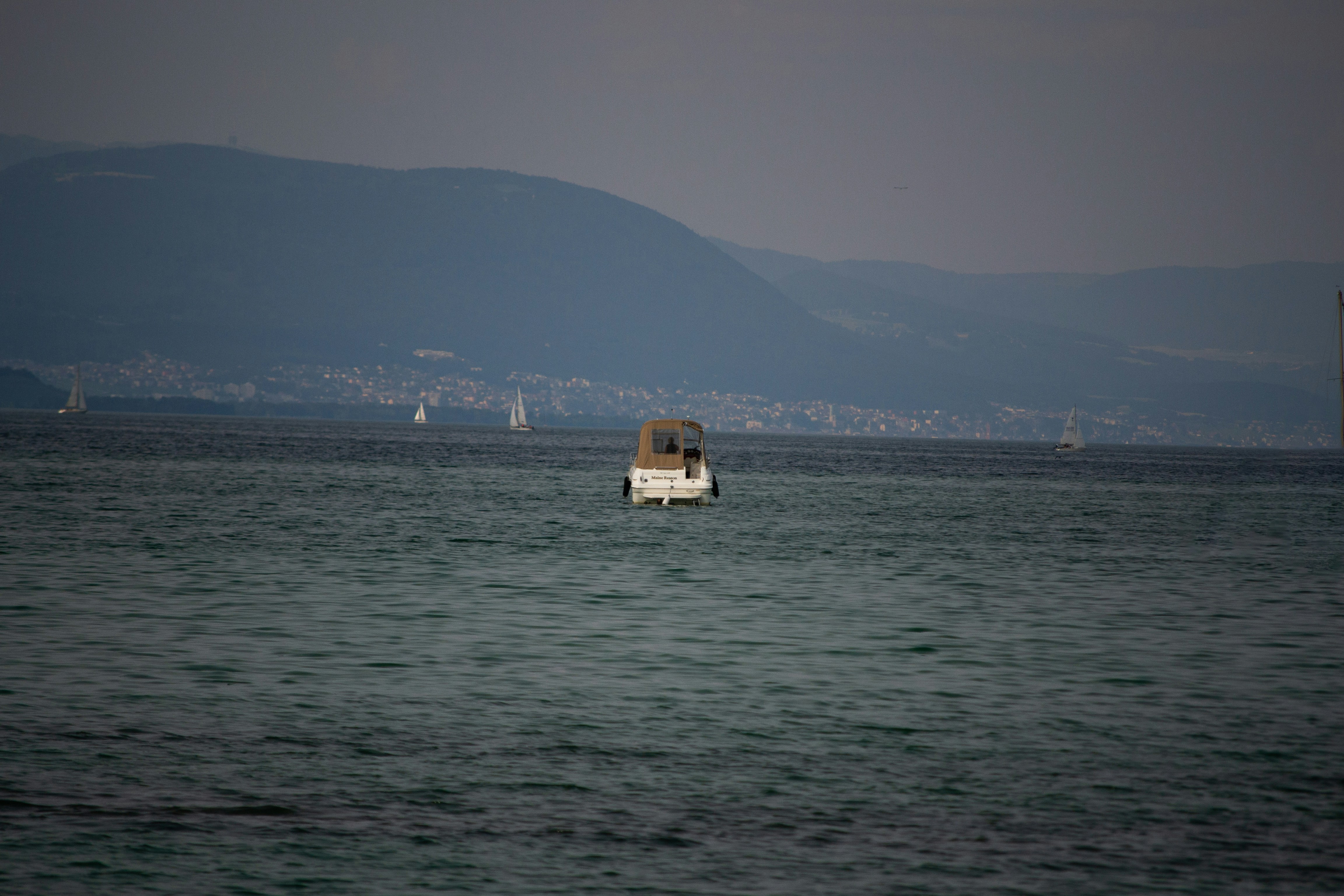 Small boat navigating calm lake against a backdrop of distant hills under a hazy sky.