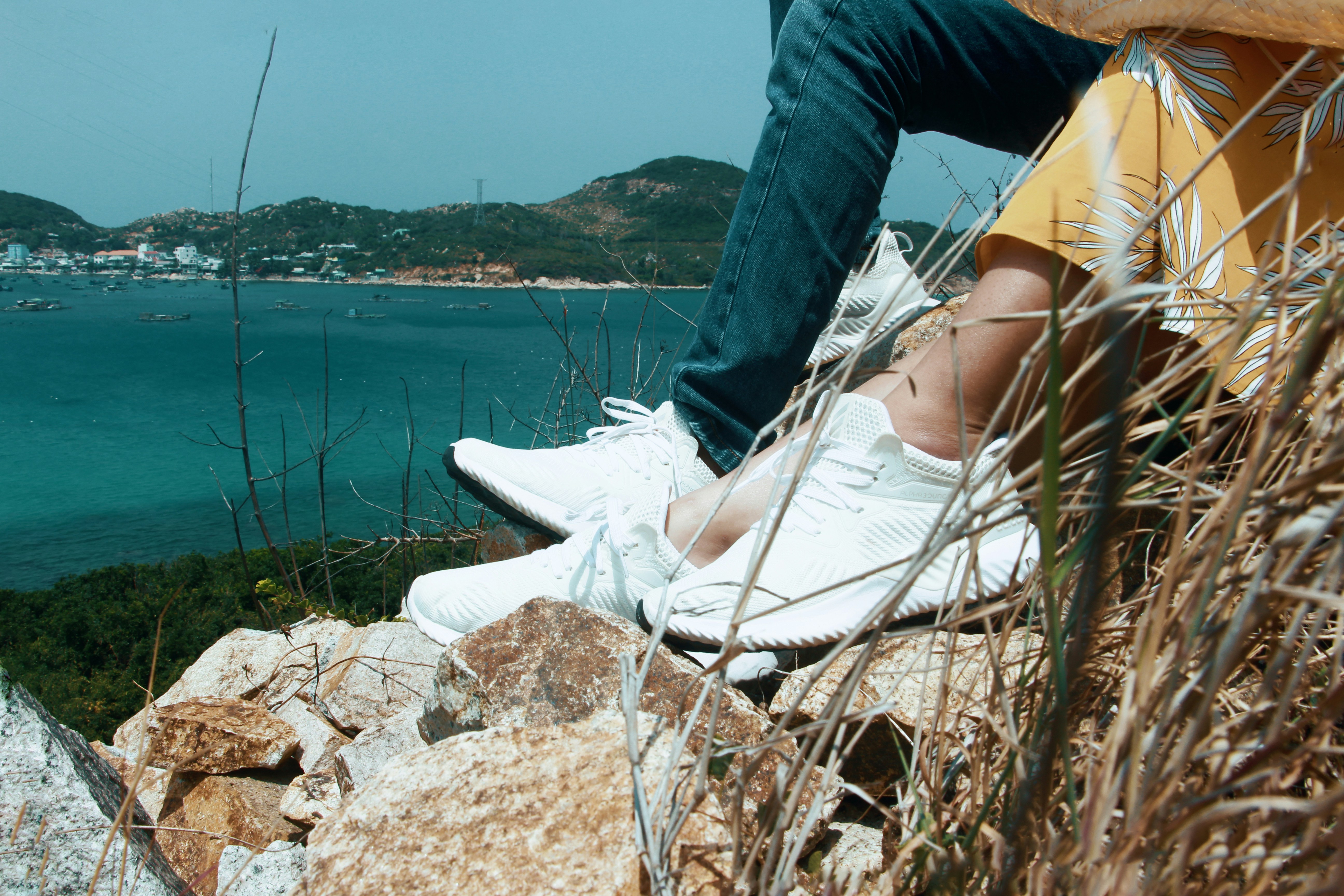 Person sitting on a rocky cliff overlooking a turquoise ocean under a clear sky.