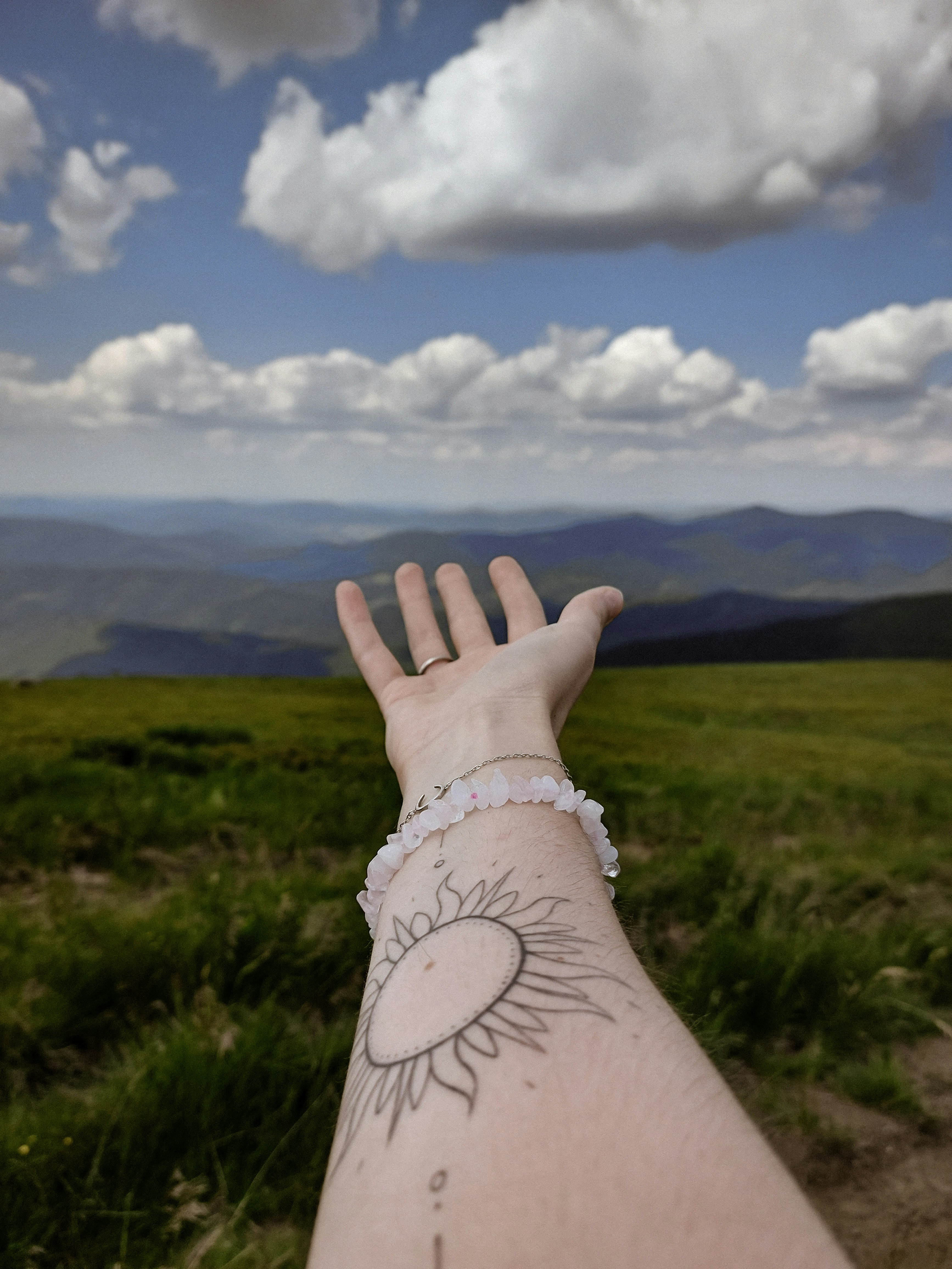 Outstretched hand toward a panoramic ridge under a cloud-sculpted sky