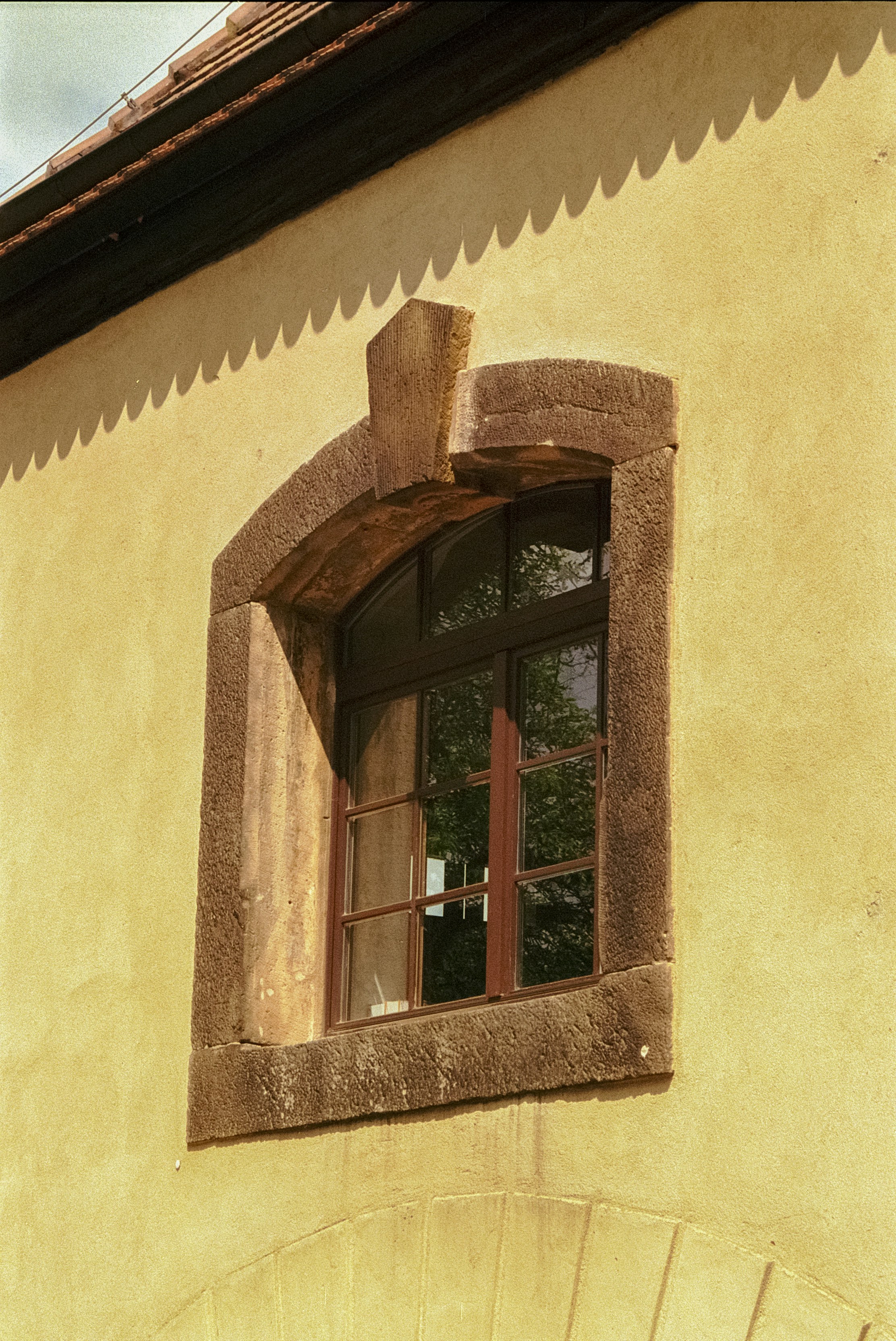 Sunlit window set in a weathered yellow wall with a stone arch and grid panes.