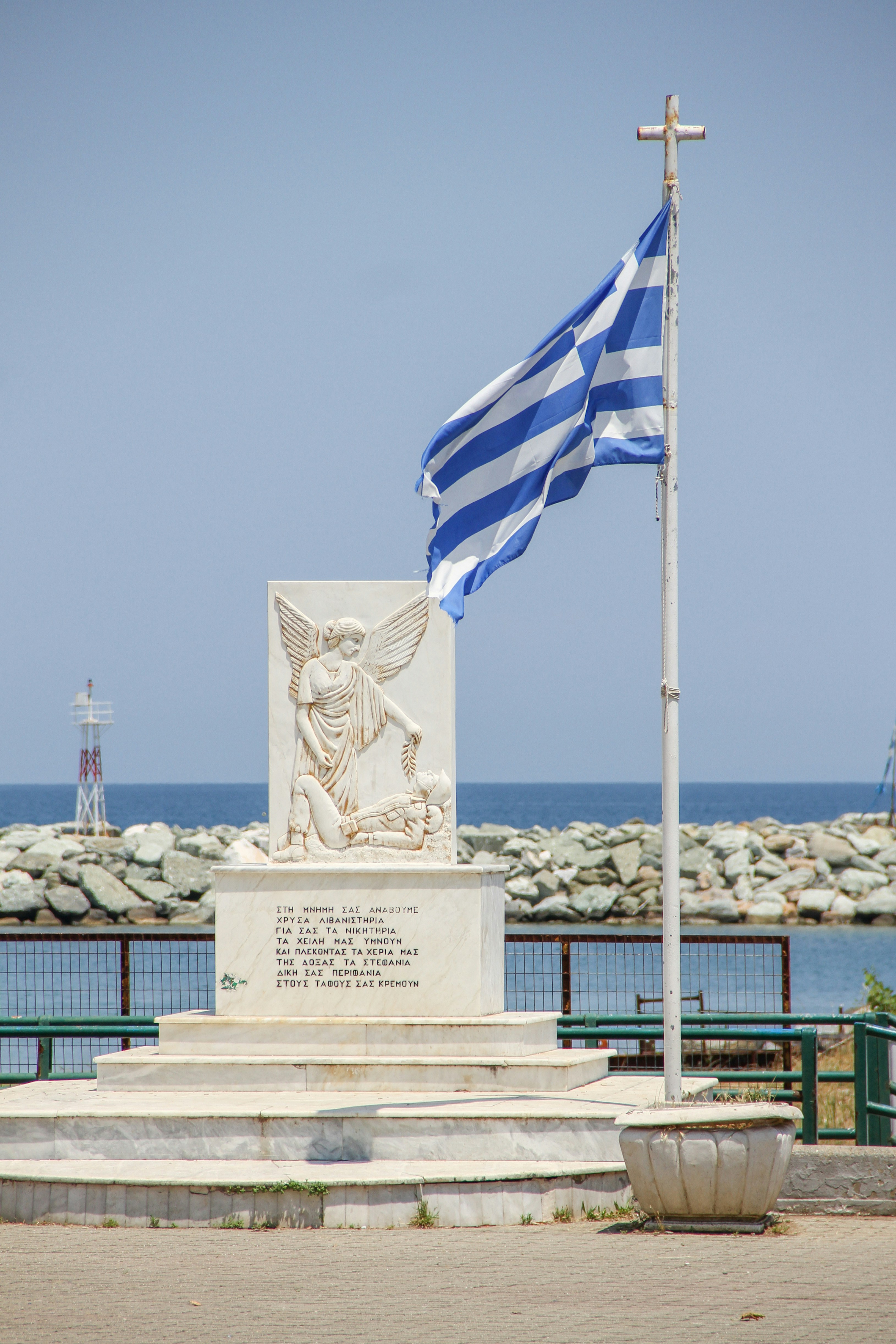 Aegean Sentinel: Marble Memorial Beside the Waving Greek Flag