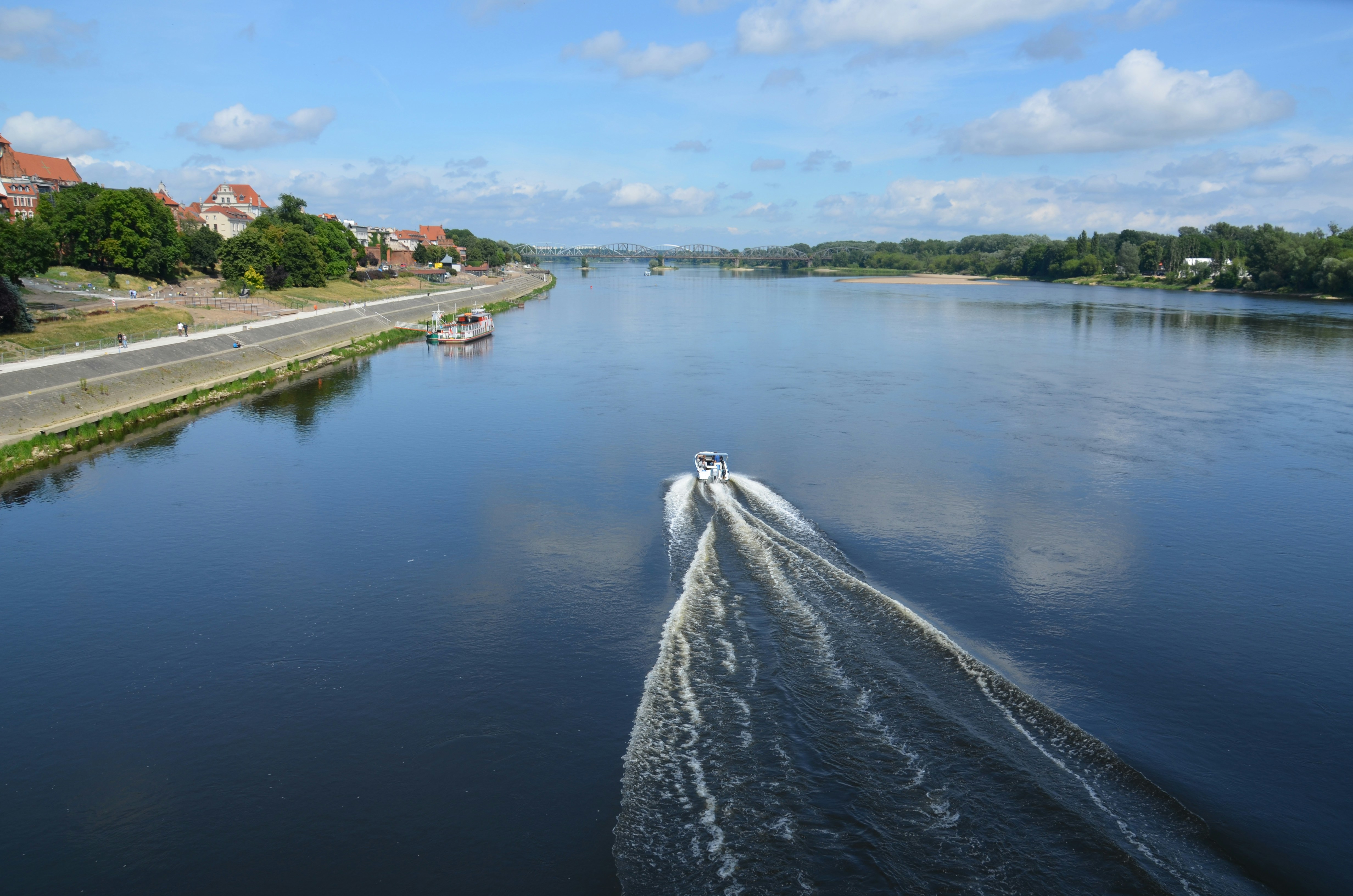 Speedboat creating ripples on a wide, calm river under a vibrant blue sky.