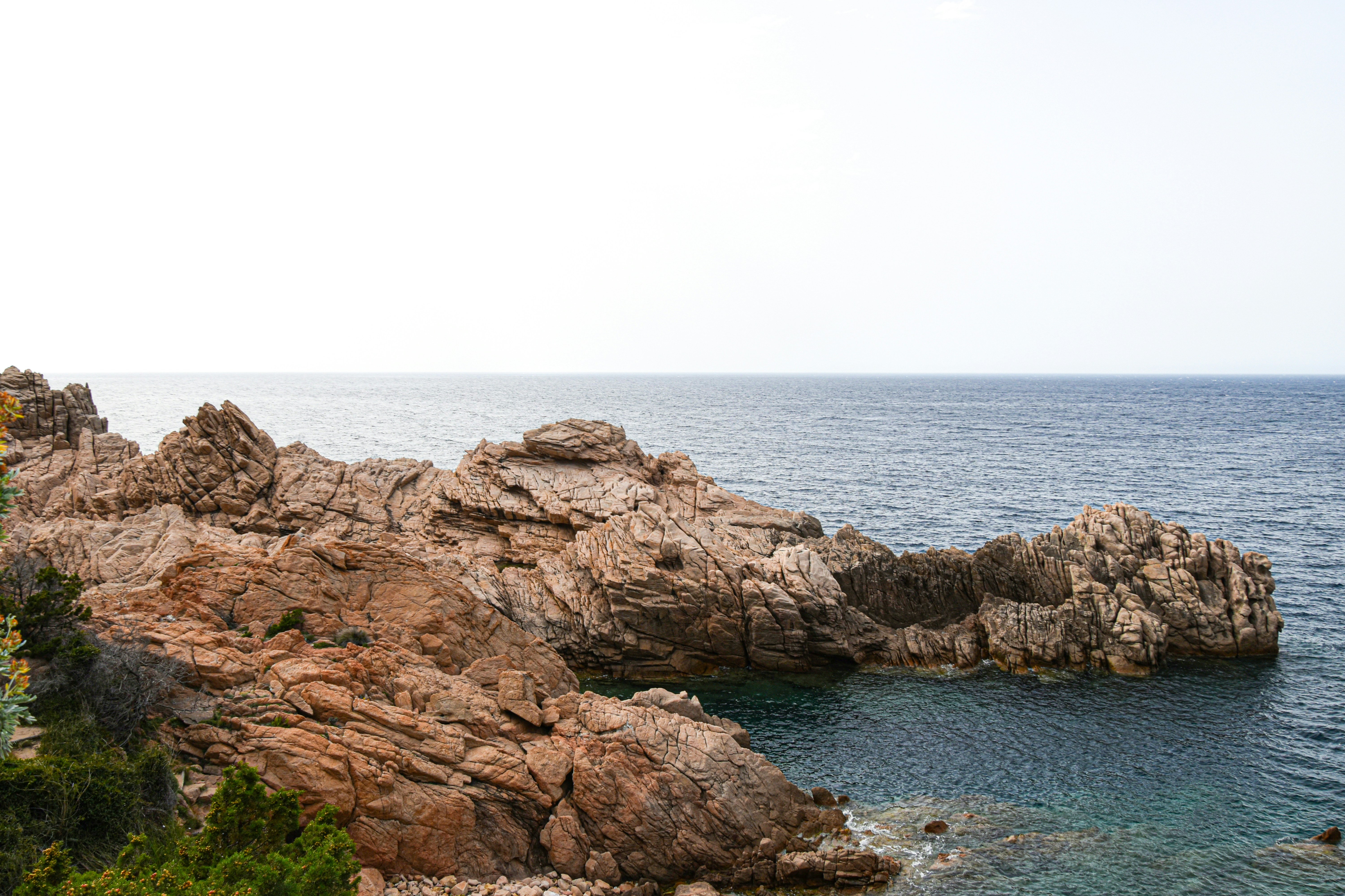 Rugged coastal rocks meet tranquil waters under a soft sky, showcasing the serene beauty of nature's formations.