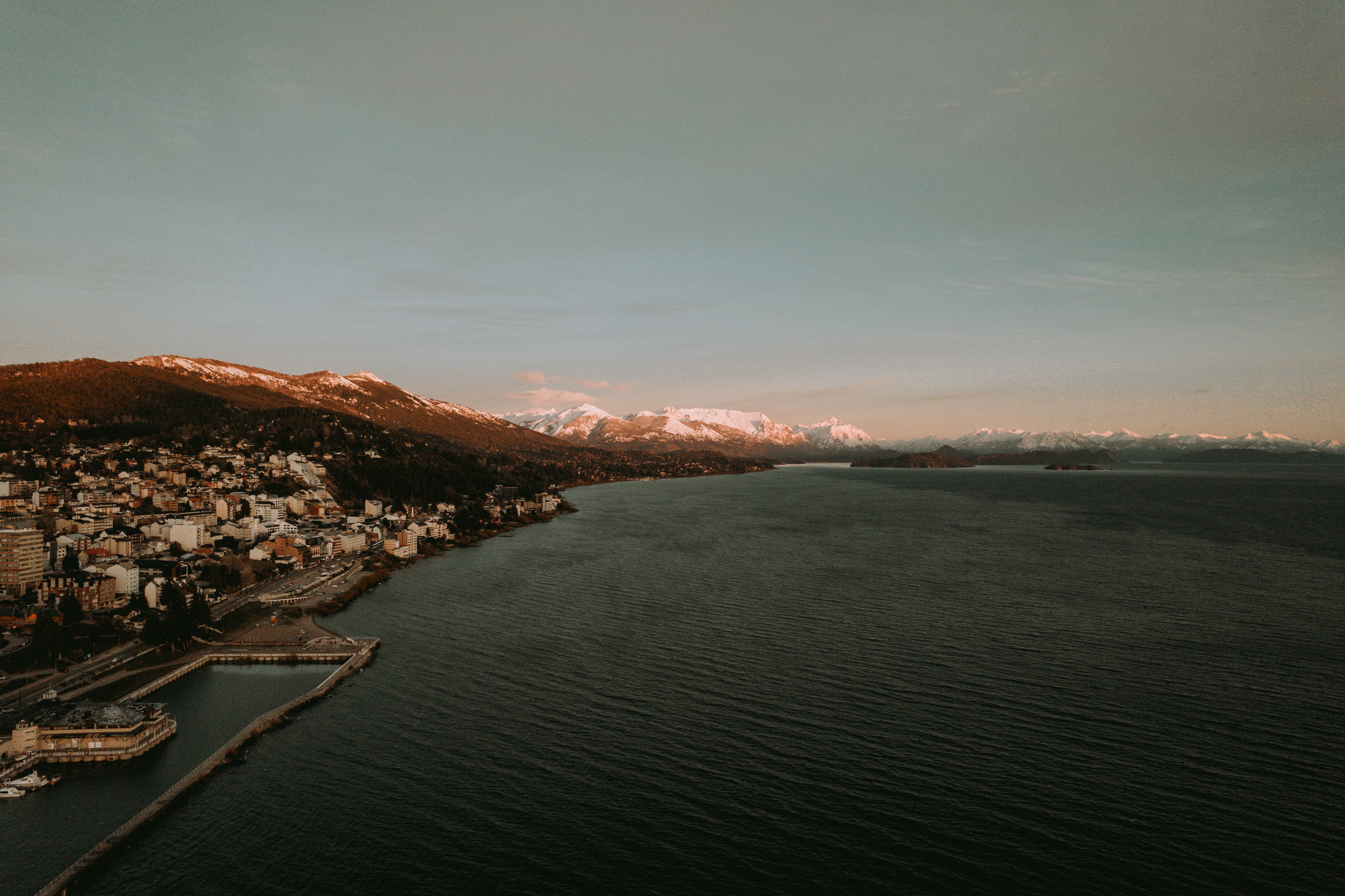 Aerial view of a coastal town beside a vast, calm sea under a softly lit sky.