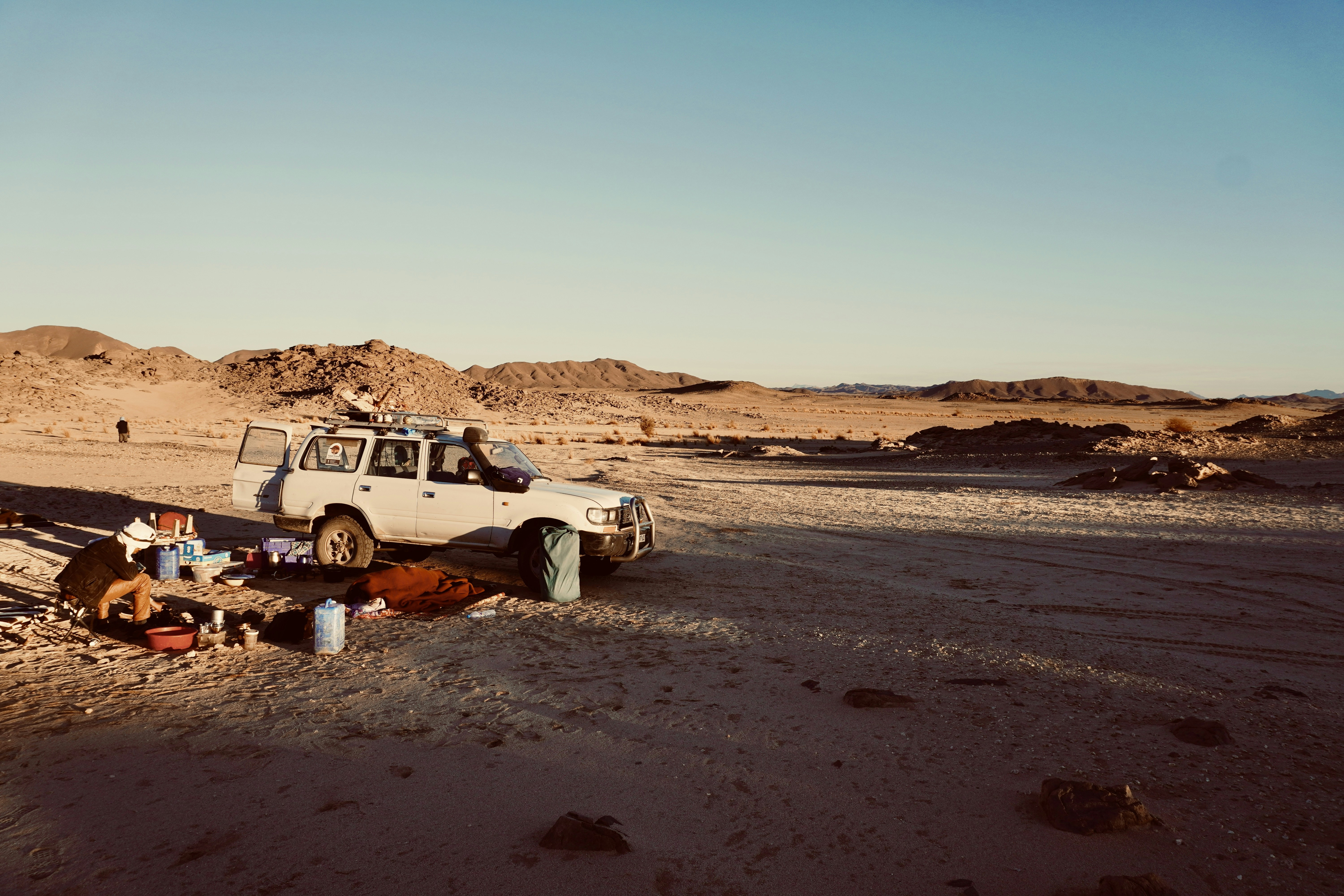 Desert Campground: A White SUV Pauses at Distant Dunes Under a Clear Sky