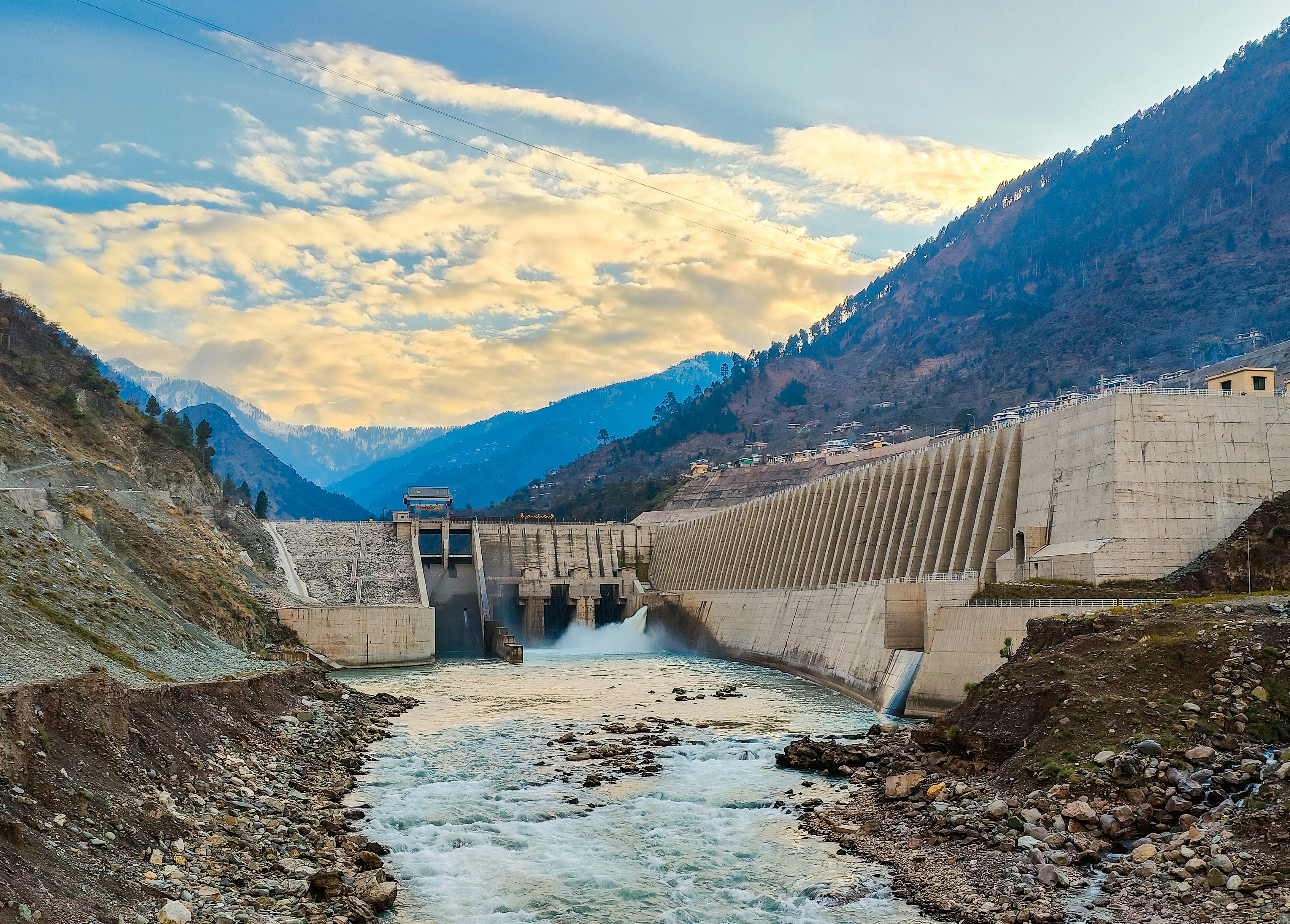 Hydroelectric dam nestled between mountainous terrain under a bright sky.