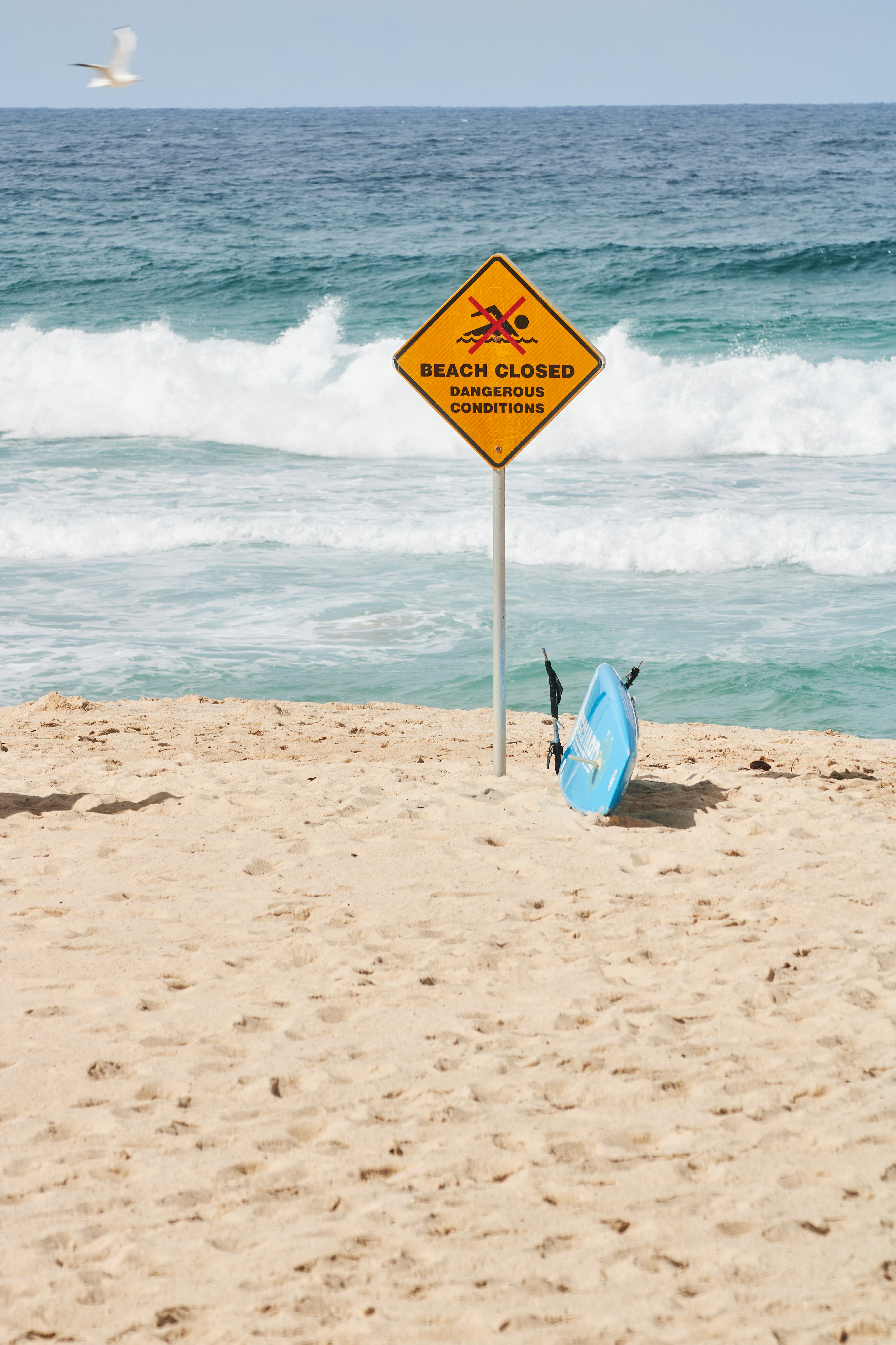 Beacon on the Shore: A Yellow Warning Guarding a Quiet Surfboard