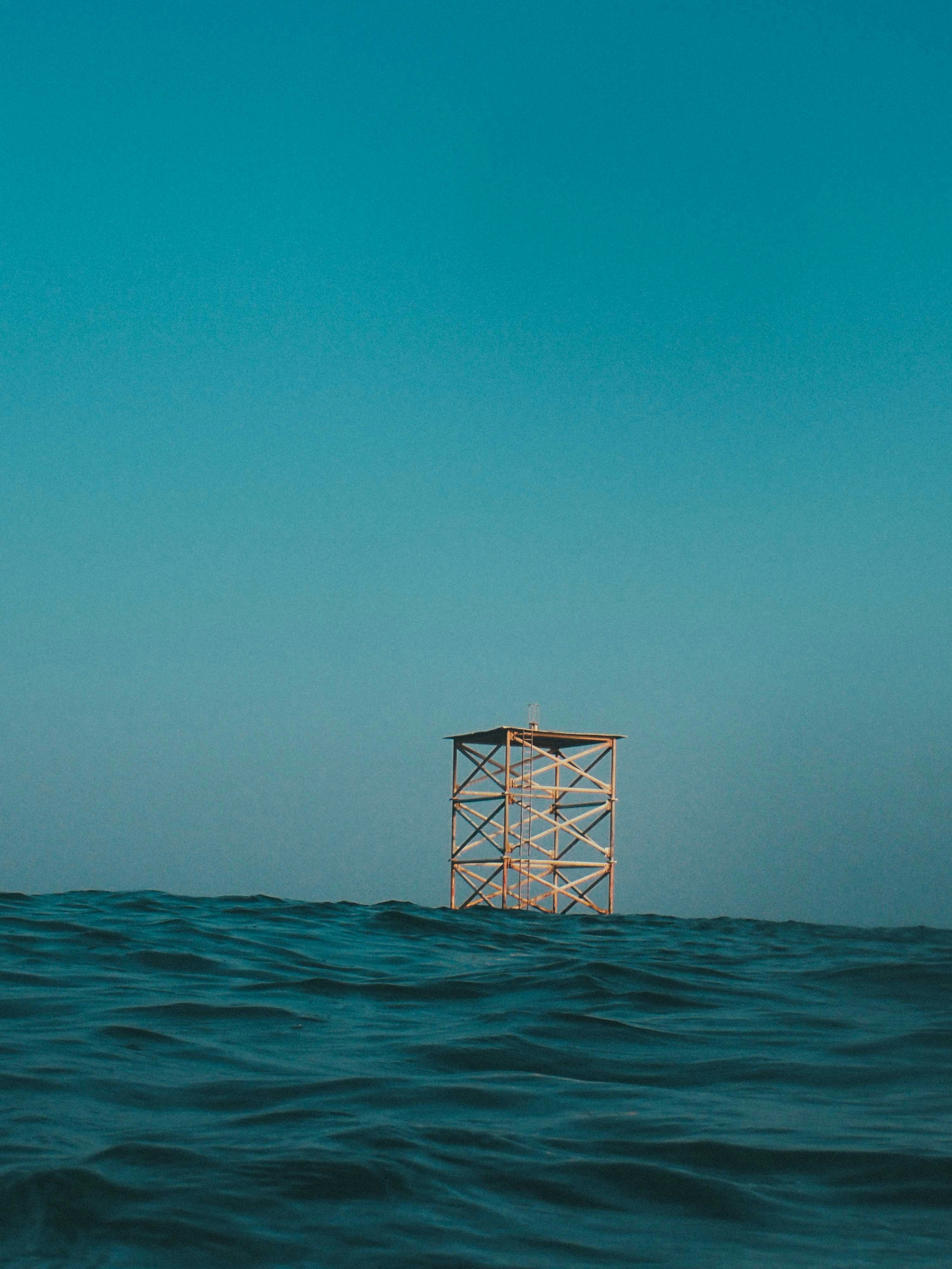 Lone offshore beacon rising above teal seas under a clear sky