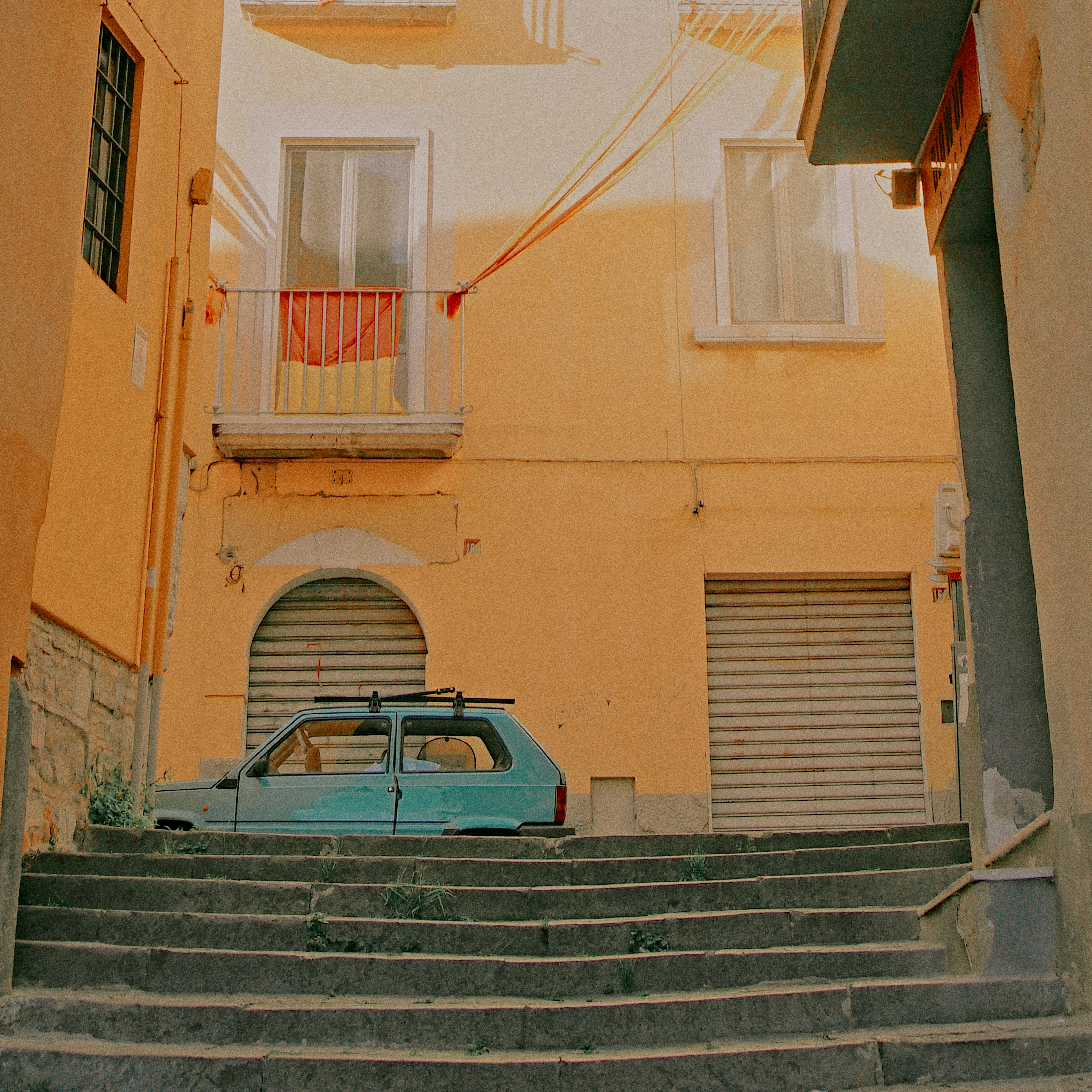 Blue Hatchback Anchoring a Sunlit Staircase Beneath Ochre Facades