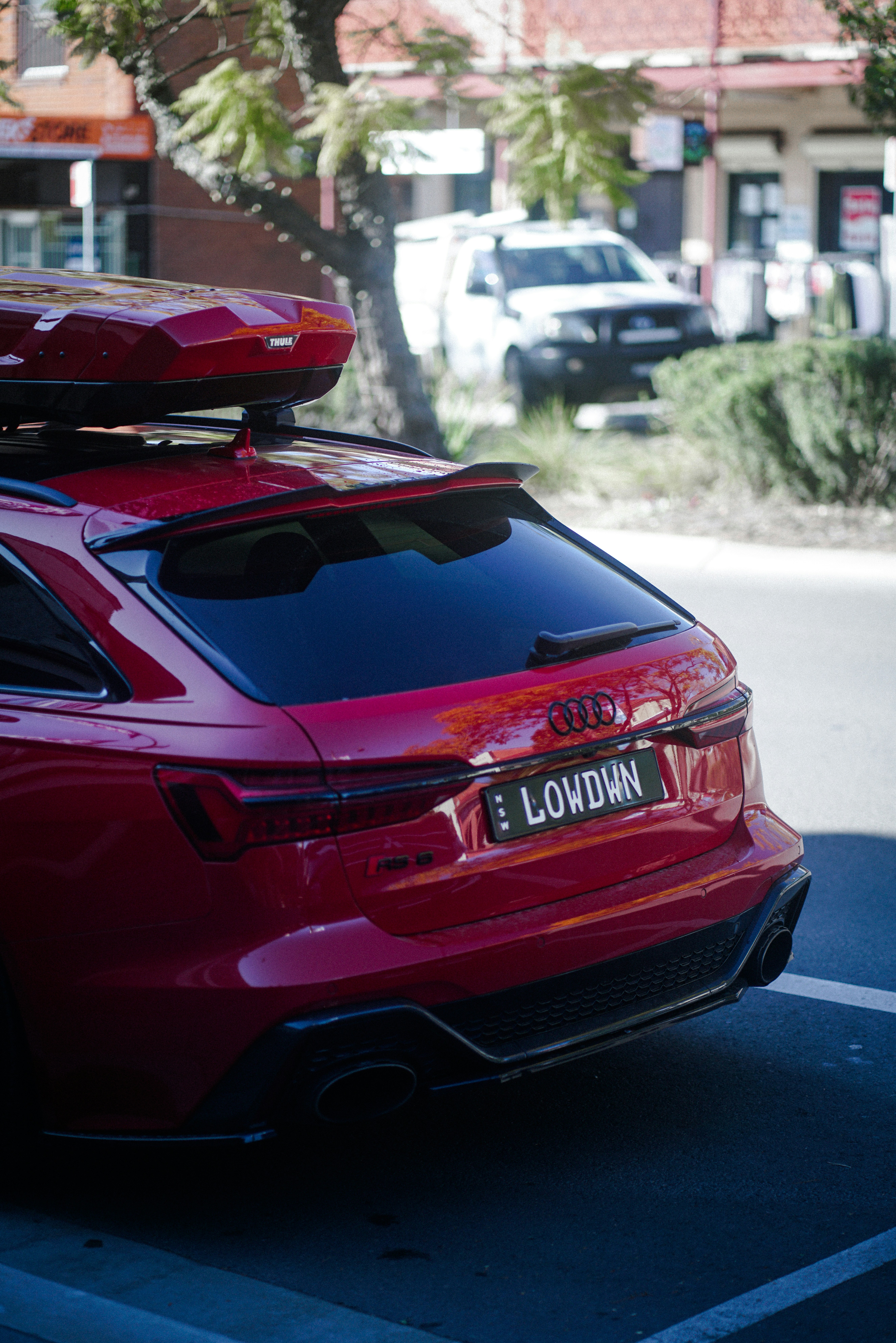 Rear-Quarter Glimpse: Red Audi with Rooftop Box Anchored in a Sunlit Street