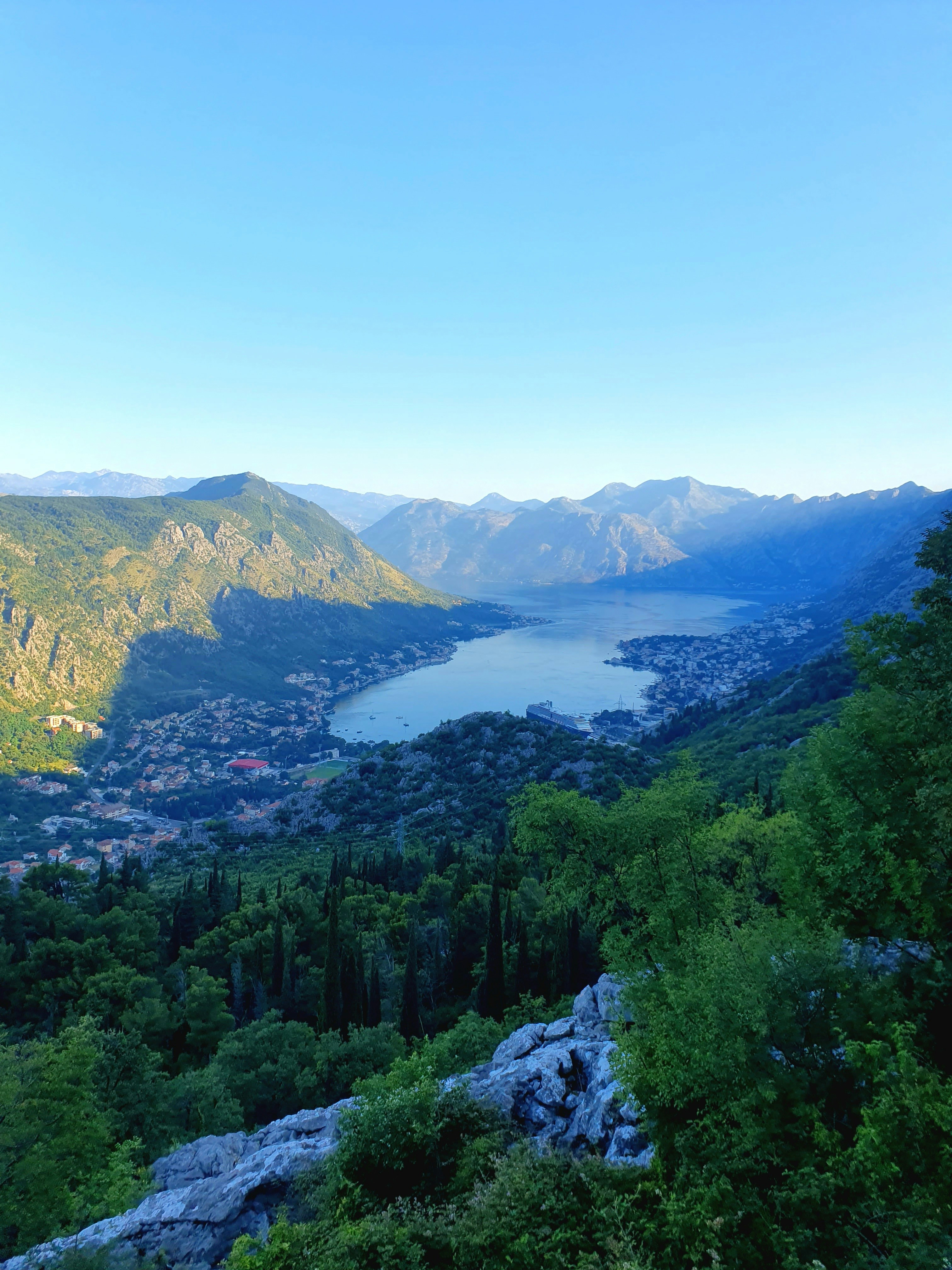 A panoramic view of Kotor Bay framed by lush greenery and rugged mountains, showcasing the tranquil waters and scattered towns below.