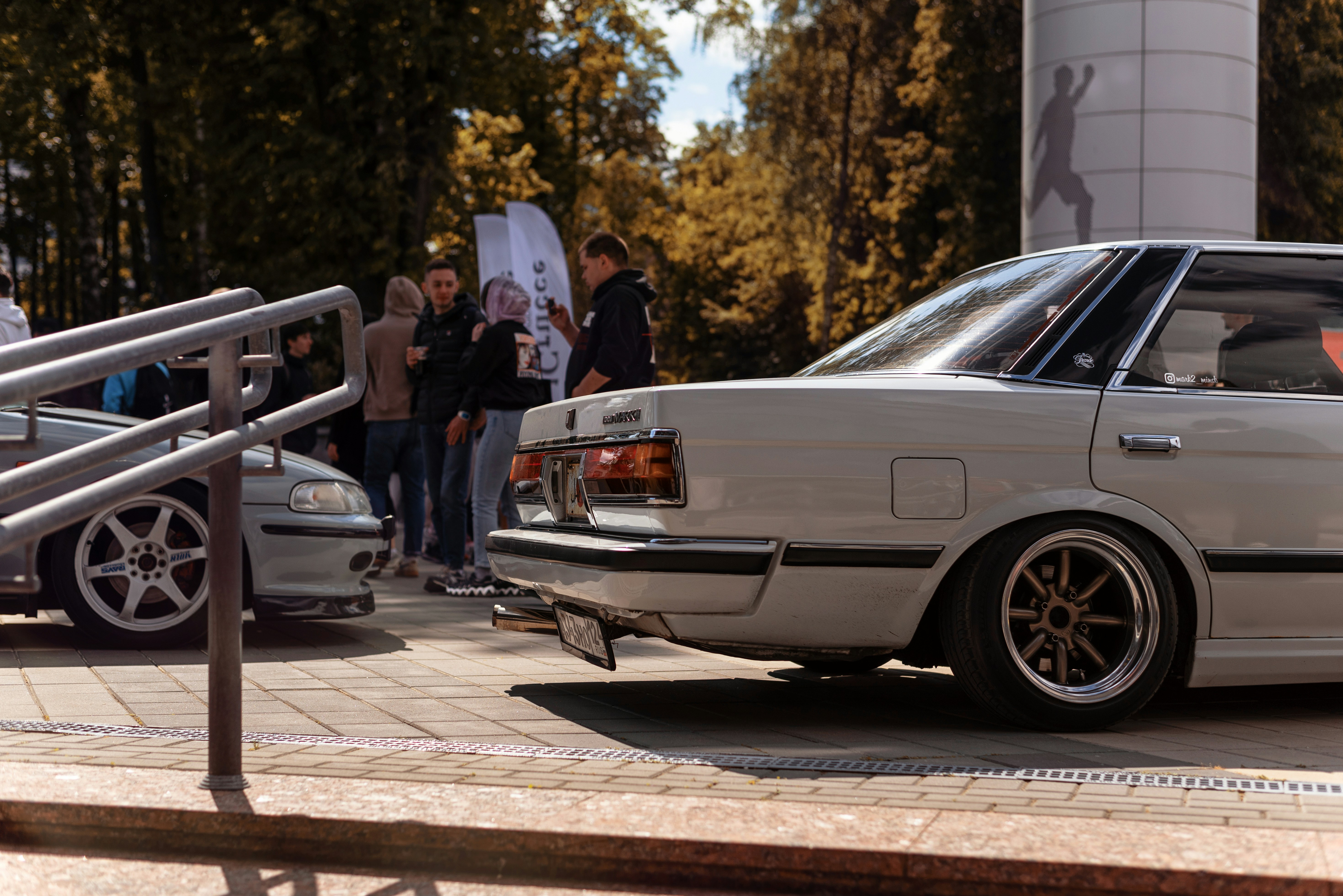 Bronze-Wheeled Classic: A White Sedan at a Sunlit Street Car Meet