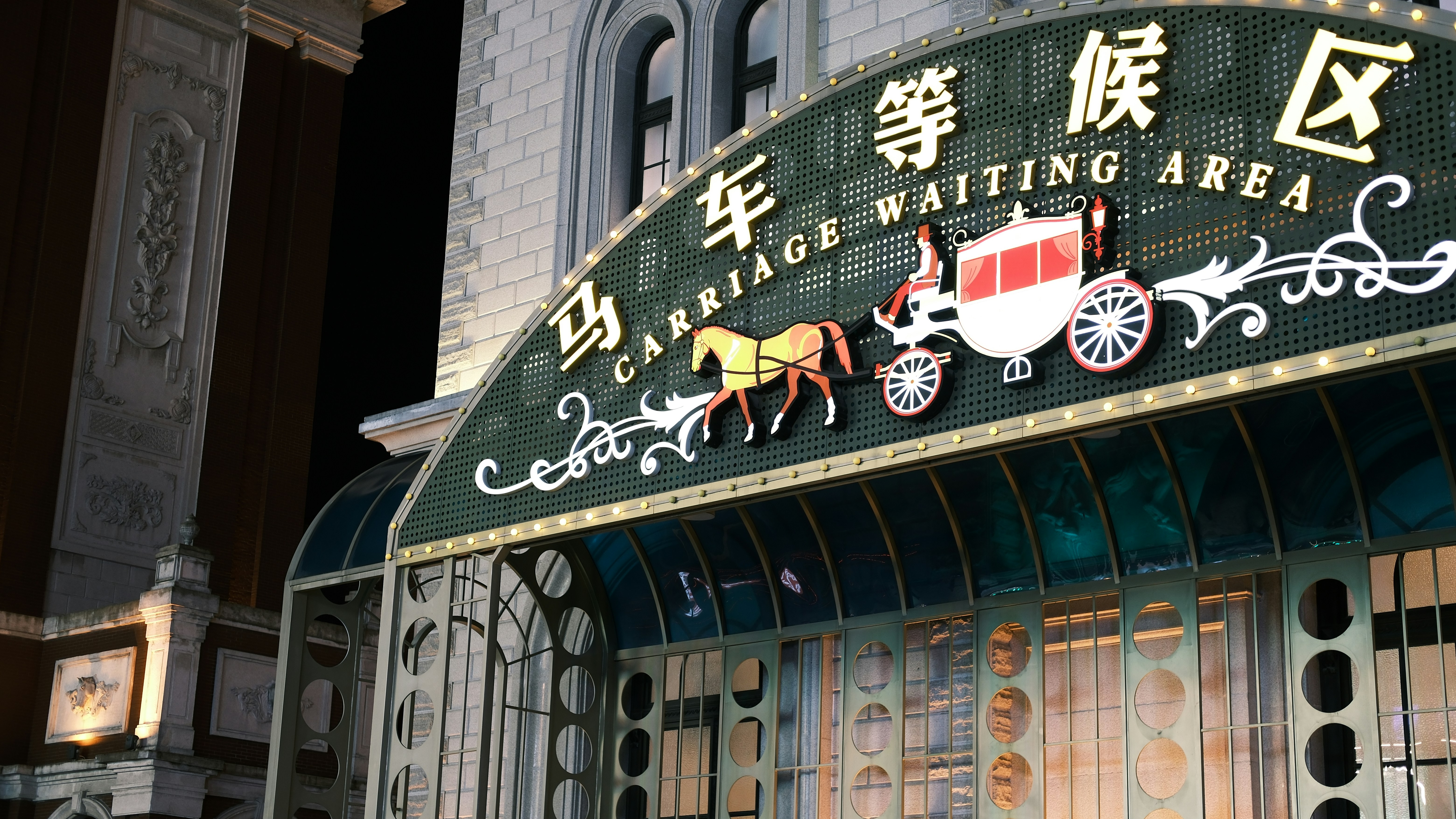 Ornately decorated waiting area sign with horse and carriage motif, illuminated under evening light.