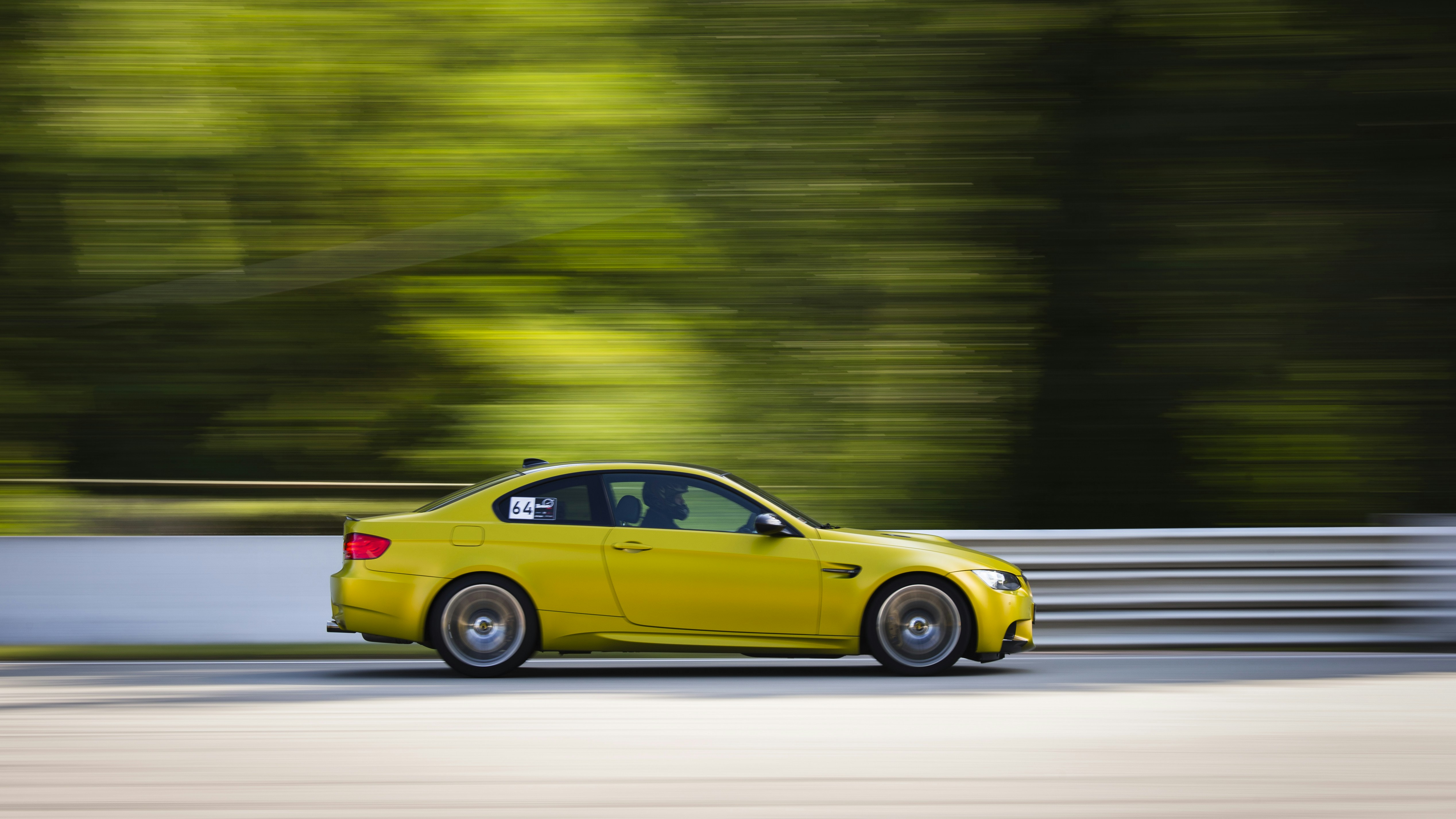 A yellow car driving down a road next to a forest photo – Free Machine ...
