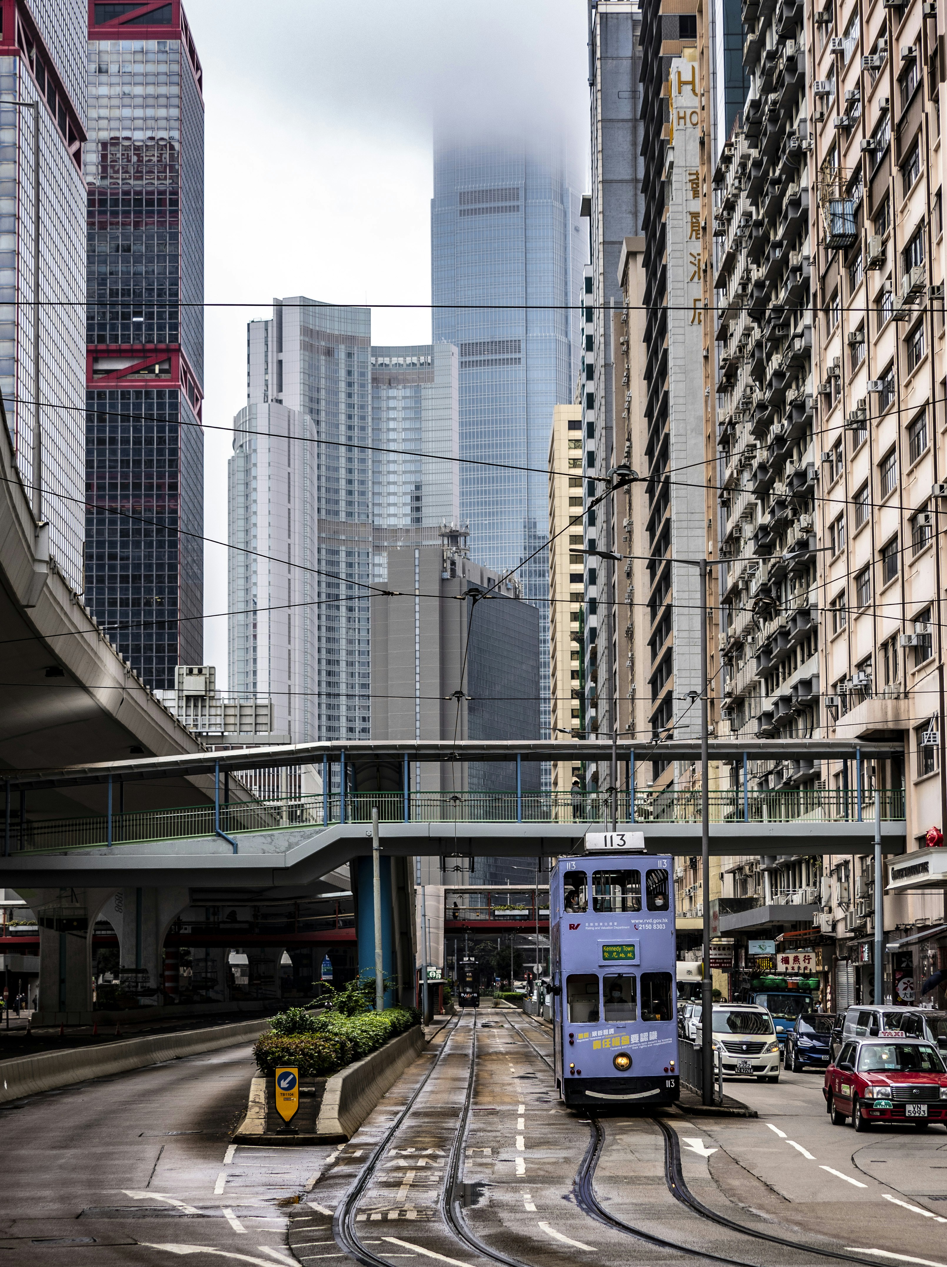 Blue tram weaving through a fog-draped city canyon