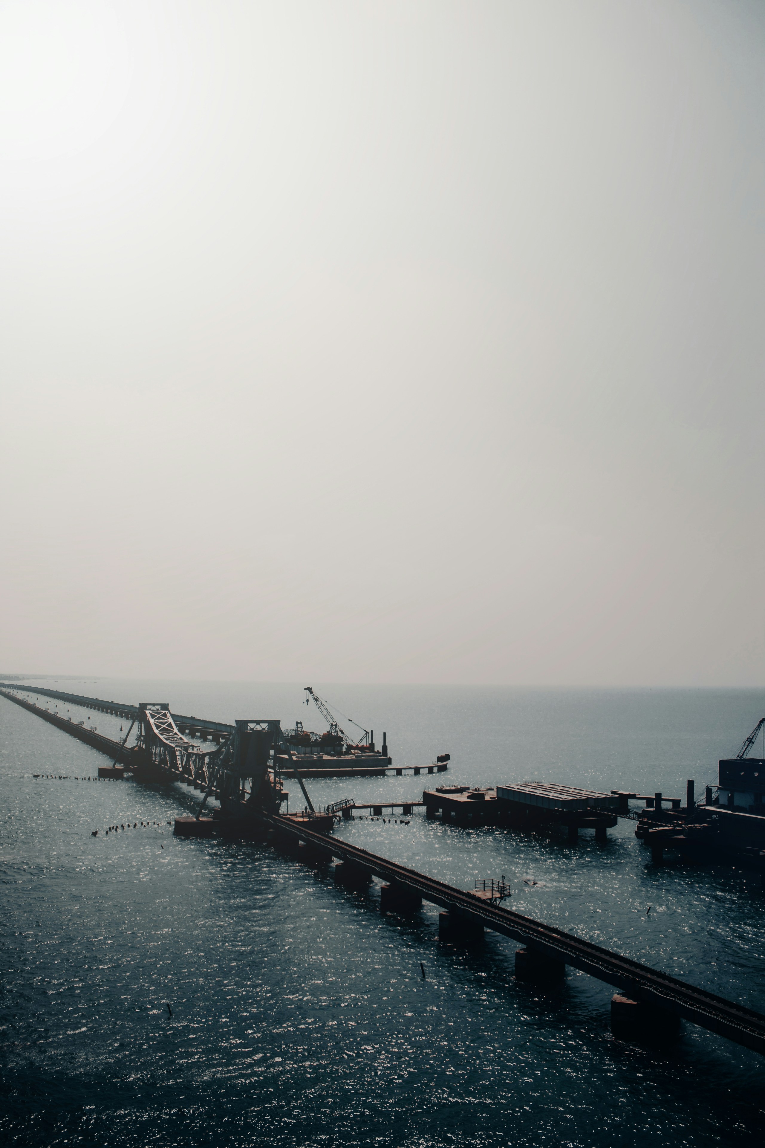 Long pier extending into the vast ocean under a hazy sky.