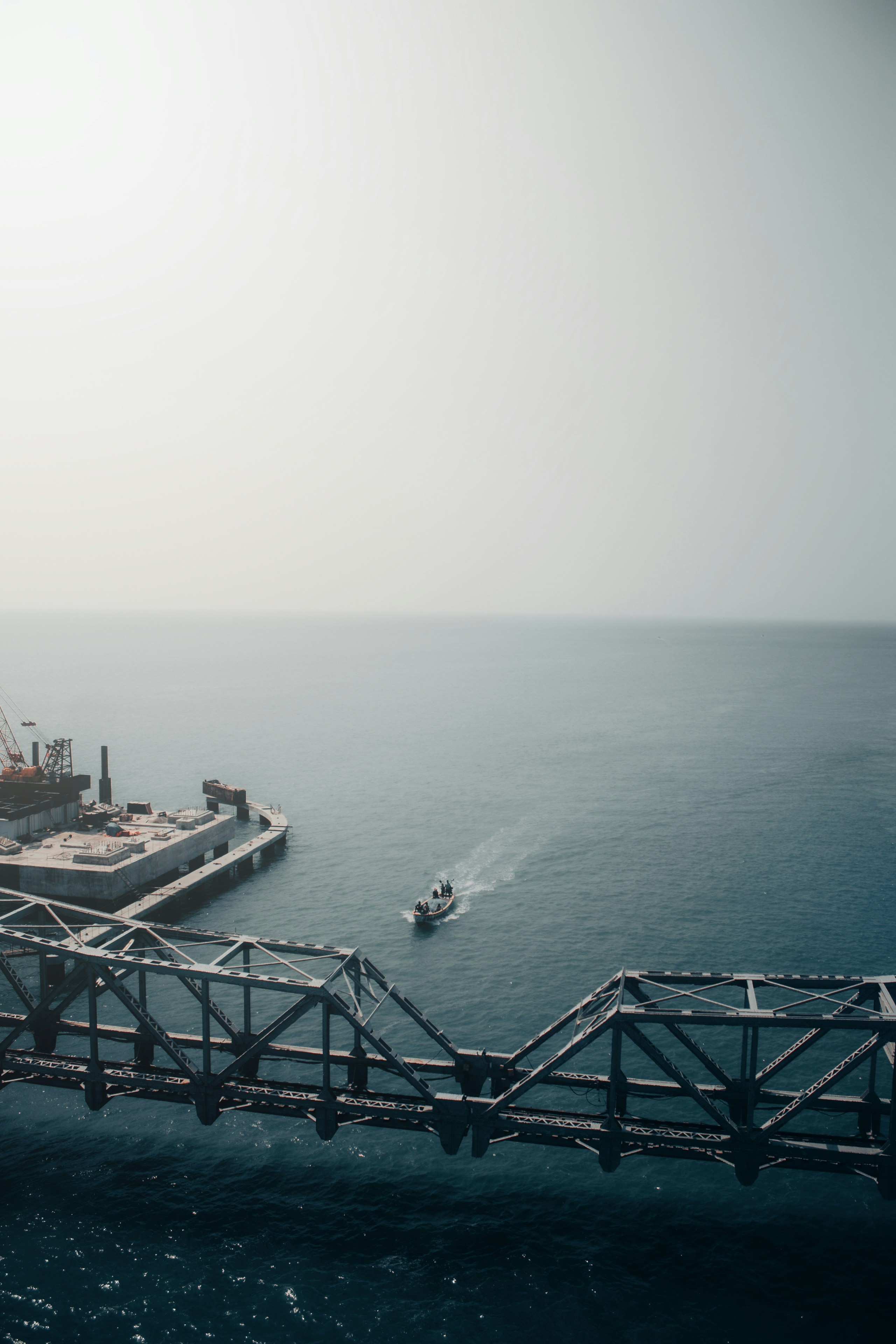 Small boat gliding across calm waters near a coastal structure under a hazy sky.