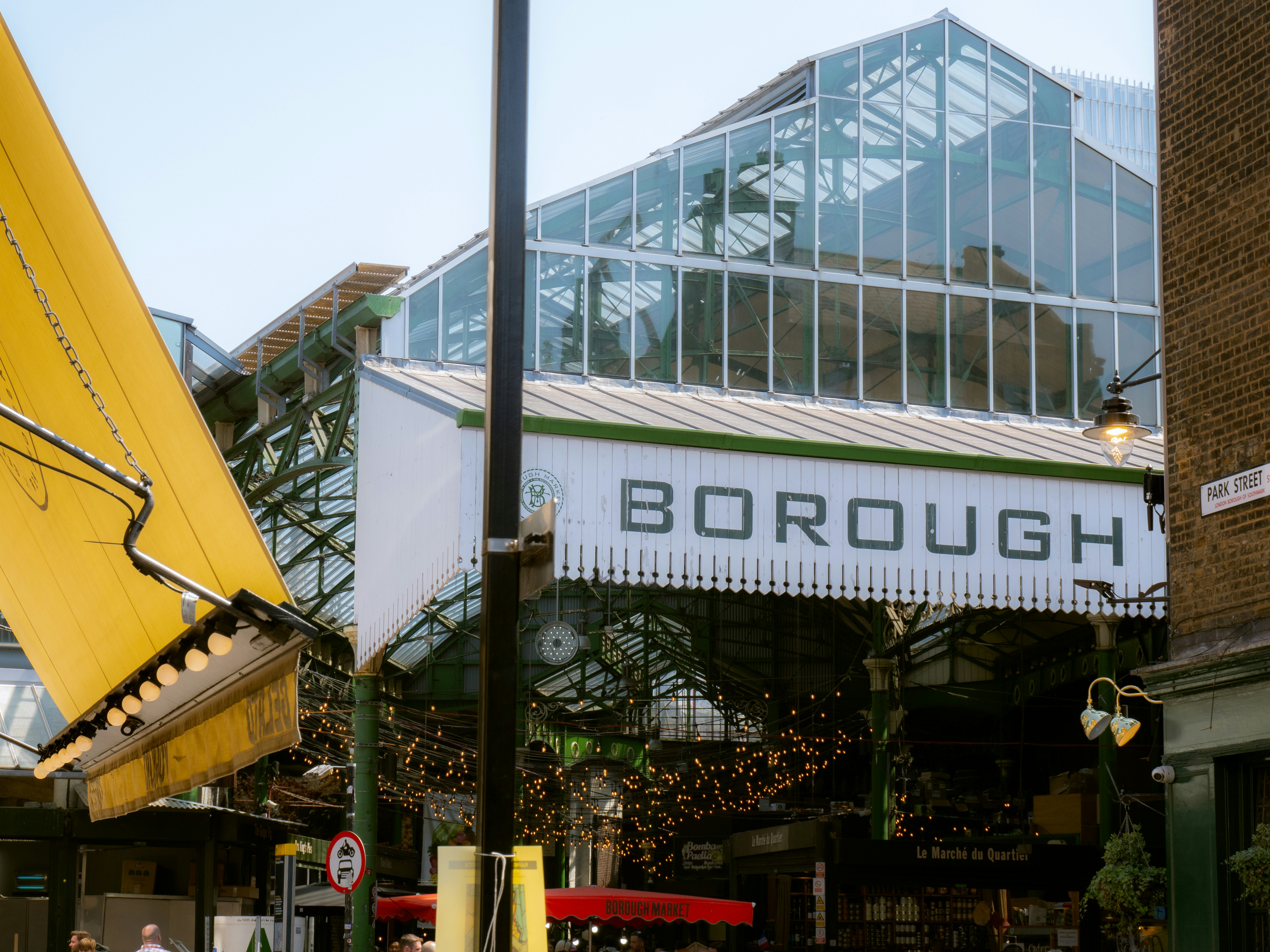 Exterior view of Borough Market entrance featuring a glass atrium, string lights, and a bright yellow awning.