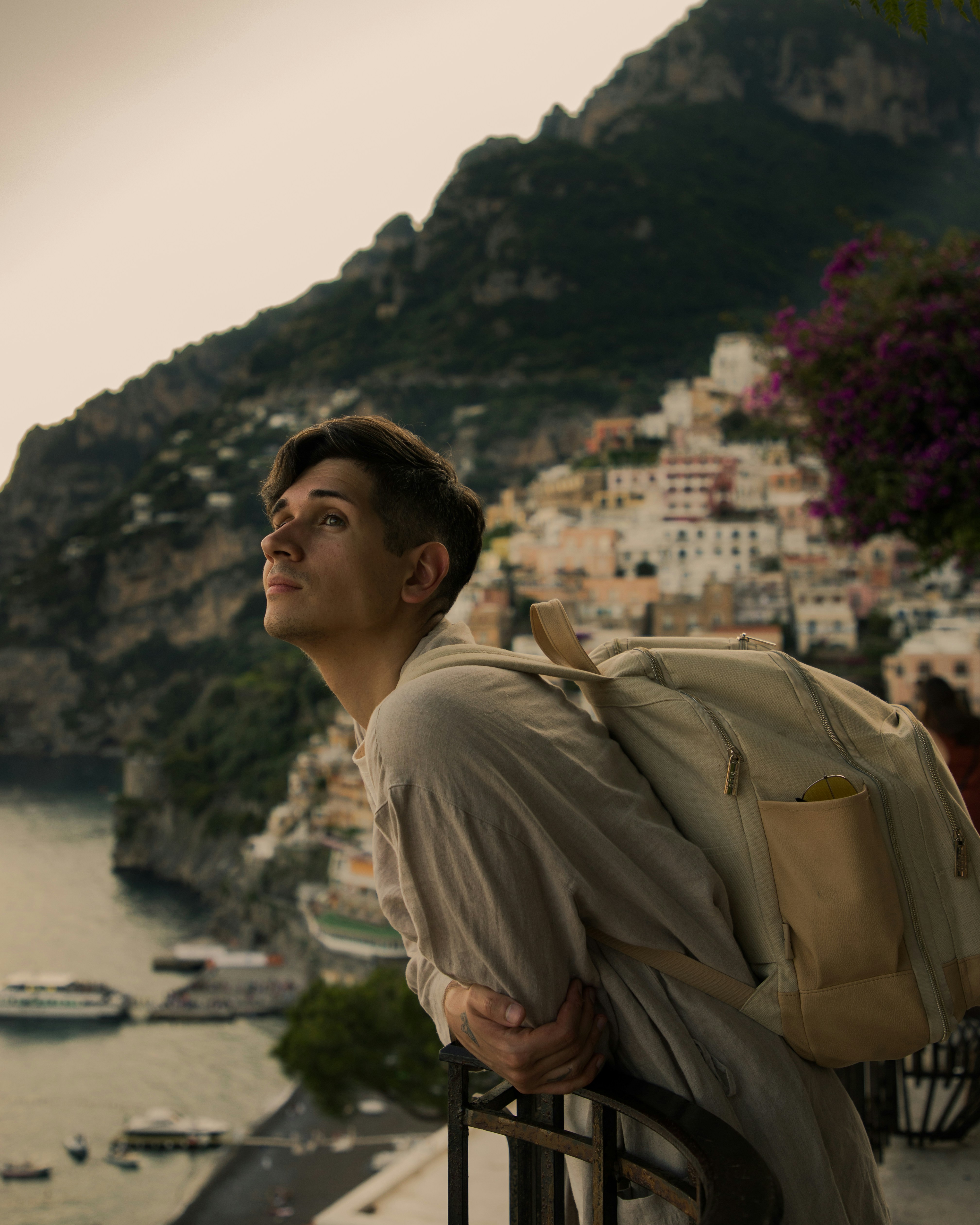 A young man leaning on a fence looking up; Behind him is the charming Positano seaside || 📸 👤: Jovan Vasiljević | a man with a backpack standing on a balcony
