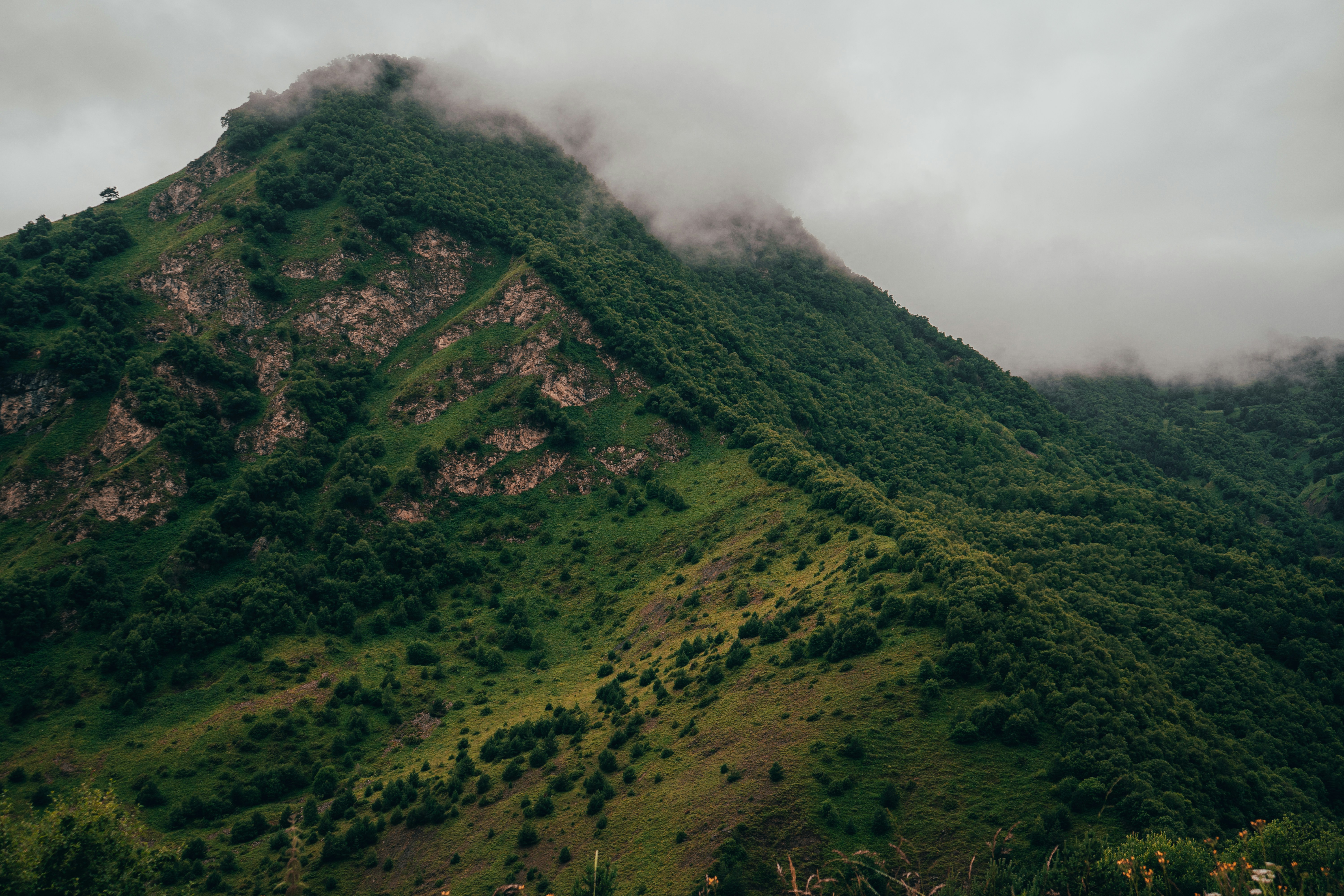 A very tall green mountain covered in clouds photo – Free North ossetia ...