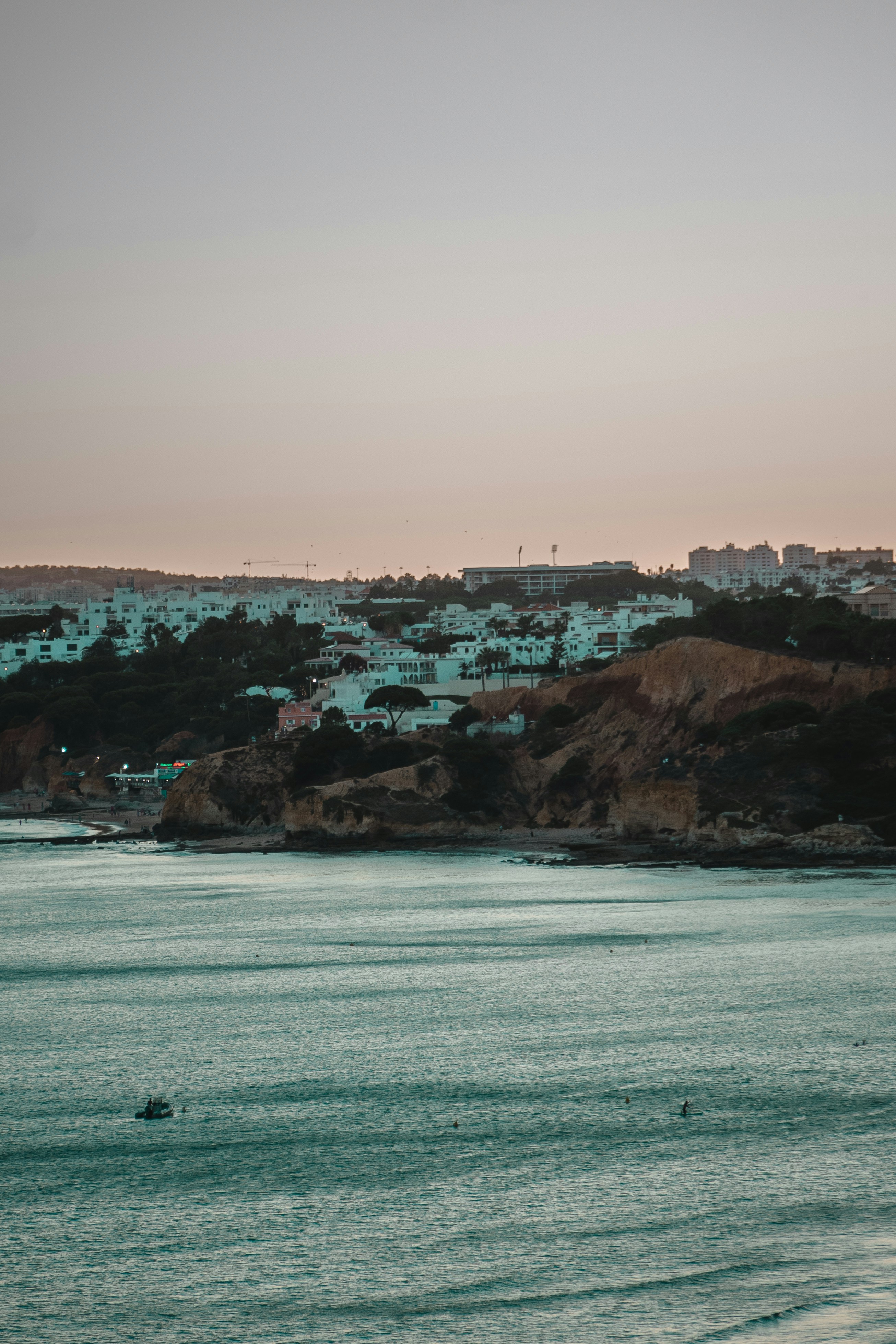 Coastal village at dusk with calm sea and pastel sky.