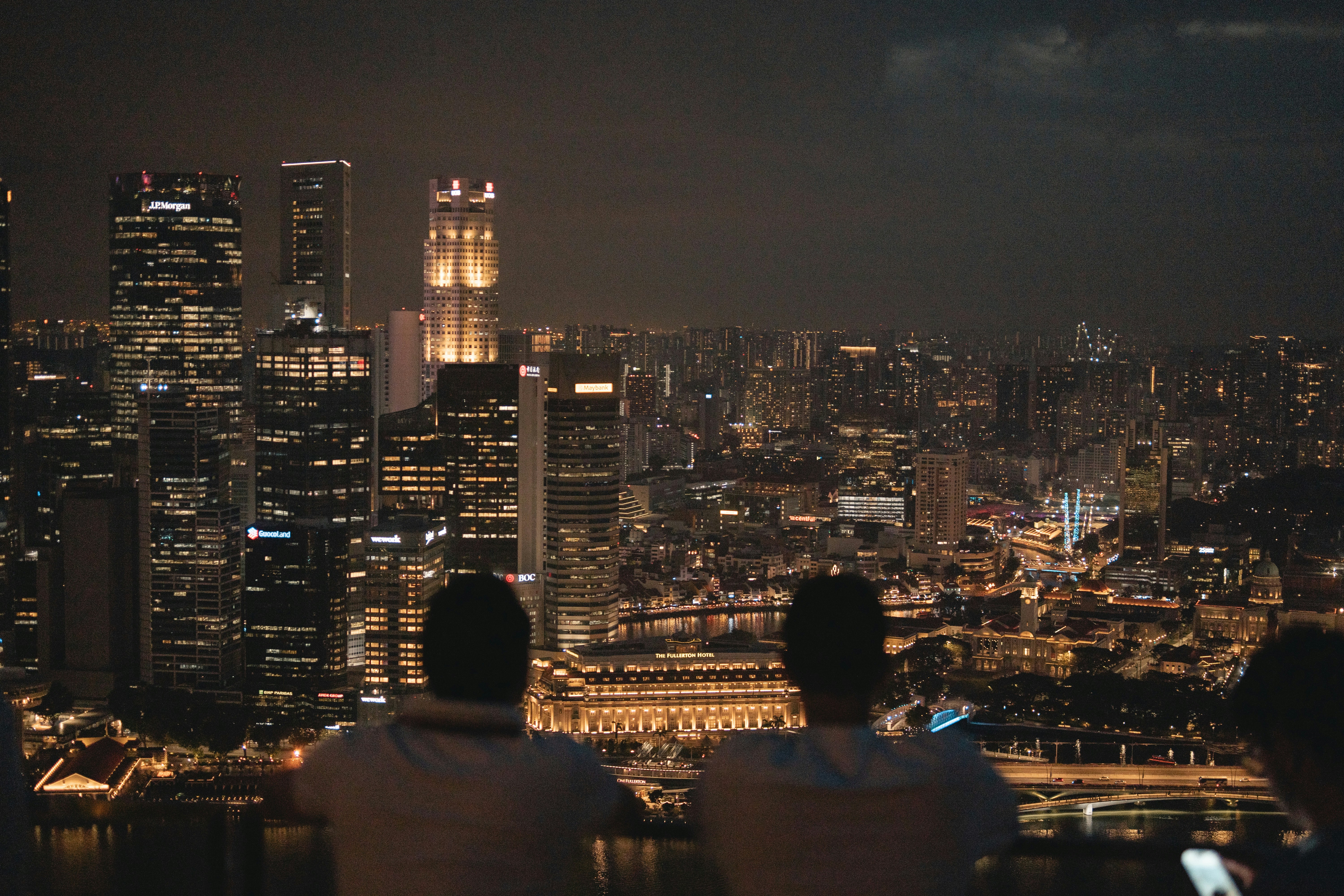 Two people sitting on a ledge overlooking a city at night photo – Free ...