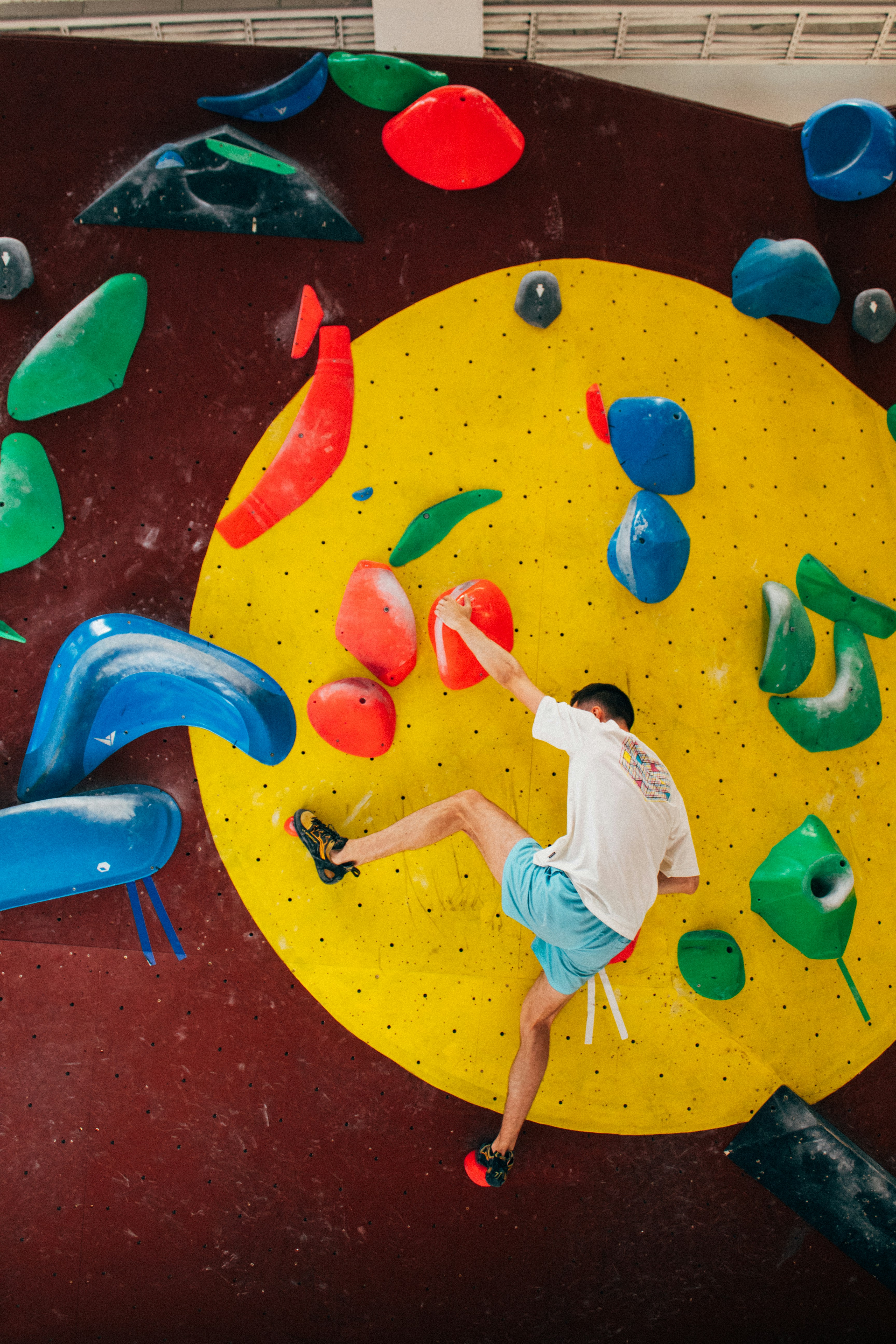 Climber in a Sunlit Bouldering Arena Reaching for a Red Handhold