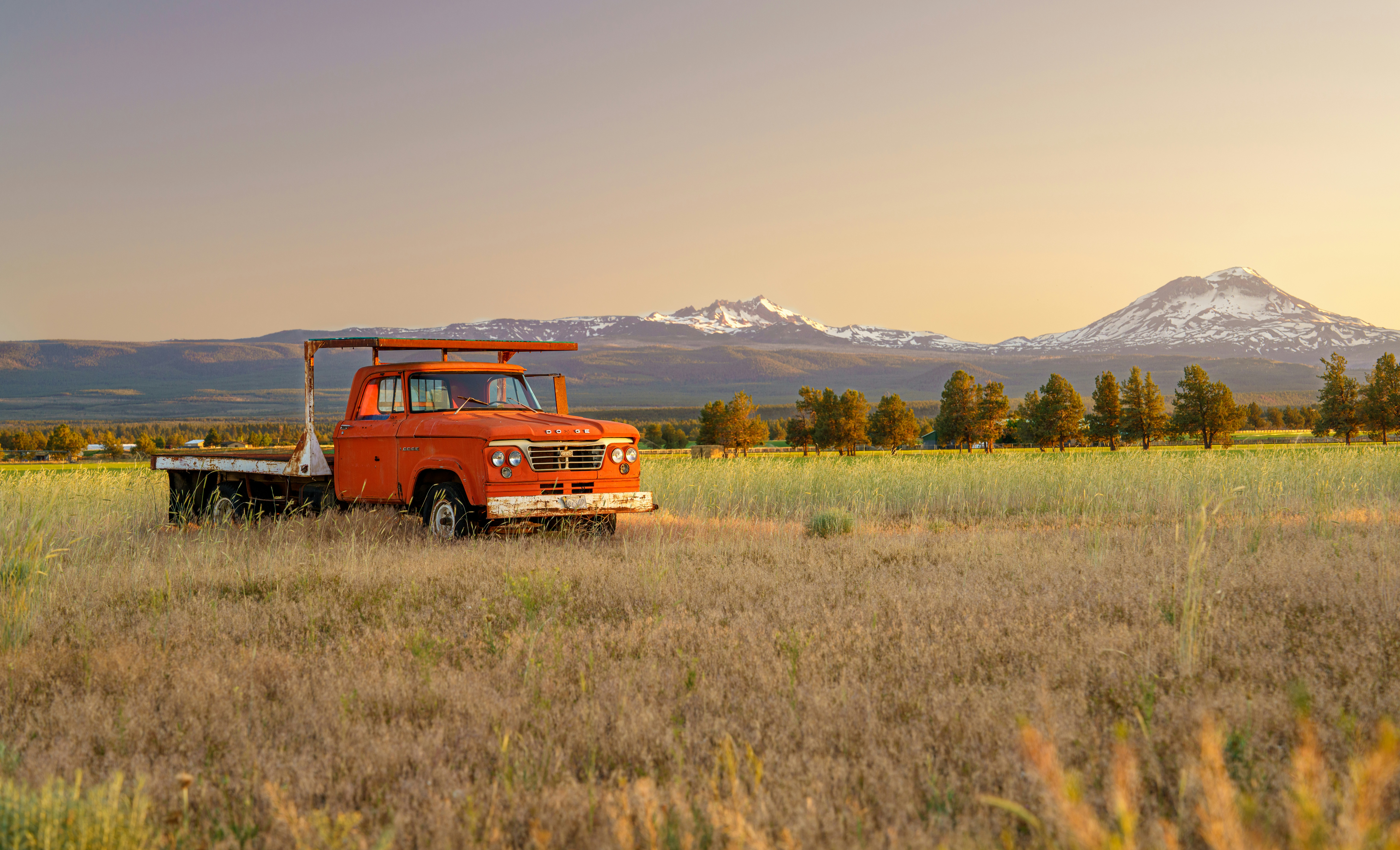 Red vintage truck in a sunlit grassland with distant snow-capped peaks