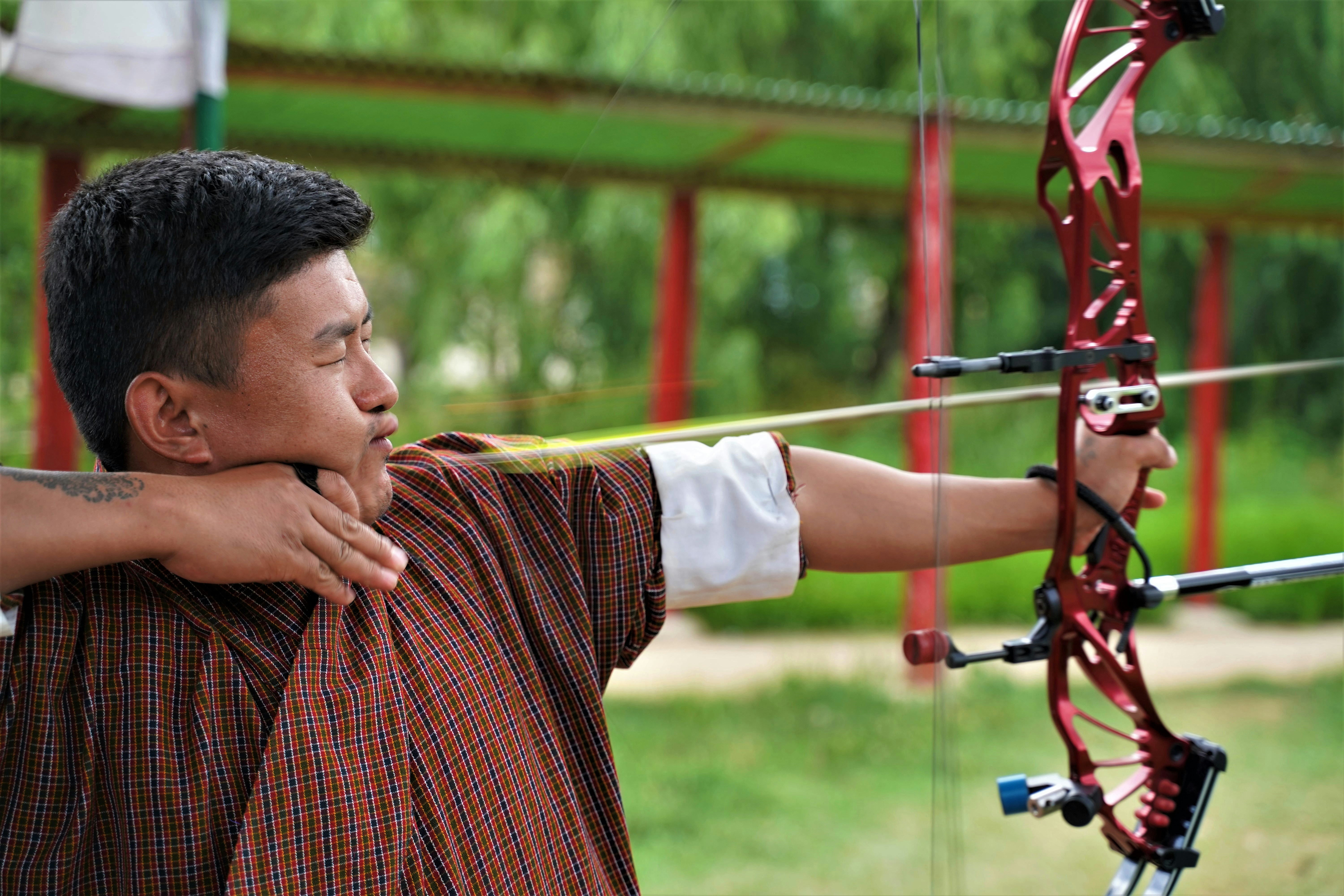 A man holding a bow and aiming it at a target photo – Free Man Image on ...