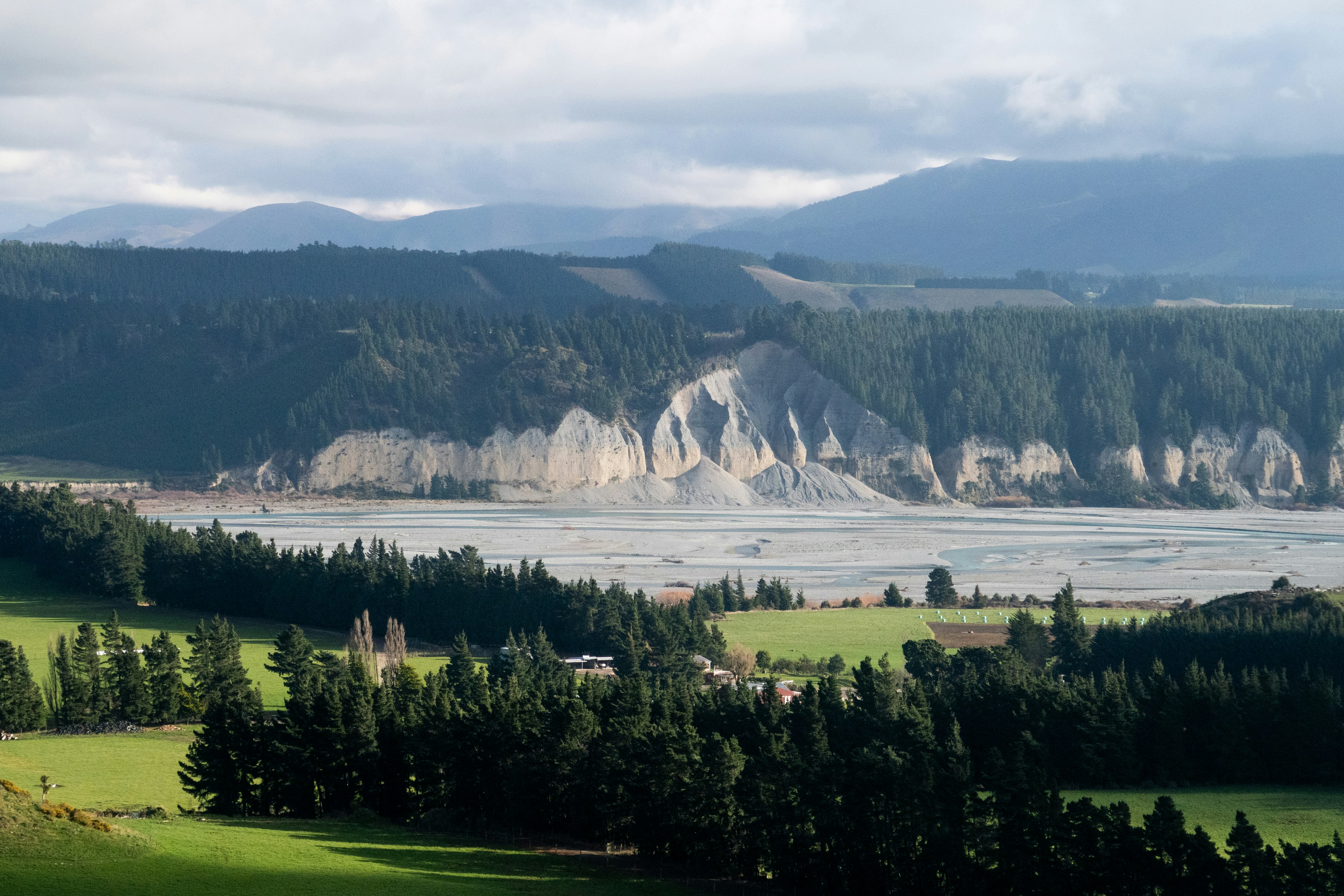Expansive view of layered cliffs and lush greenery, showcasing the contrast between geological formations and fertile land.