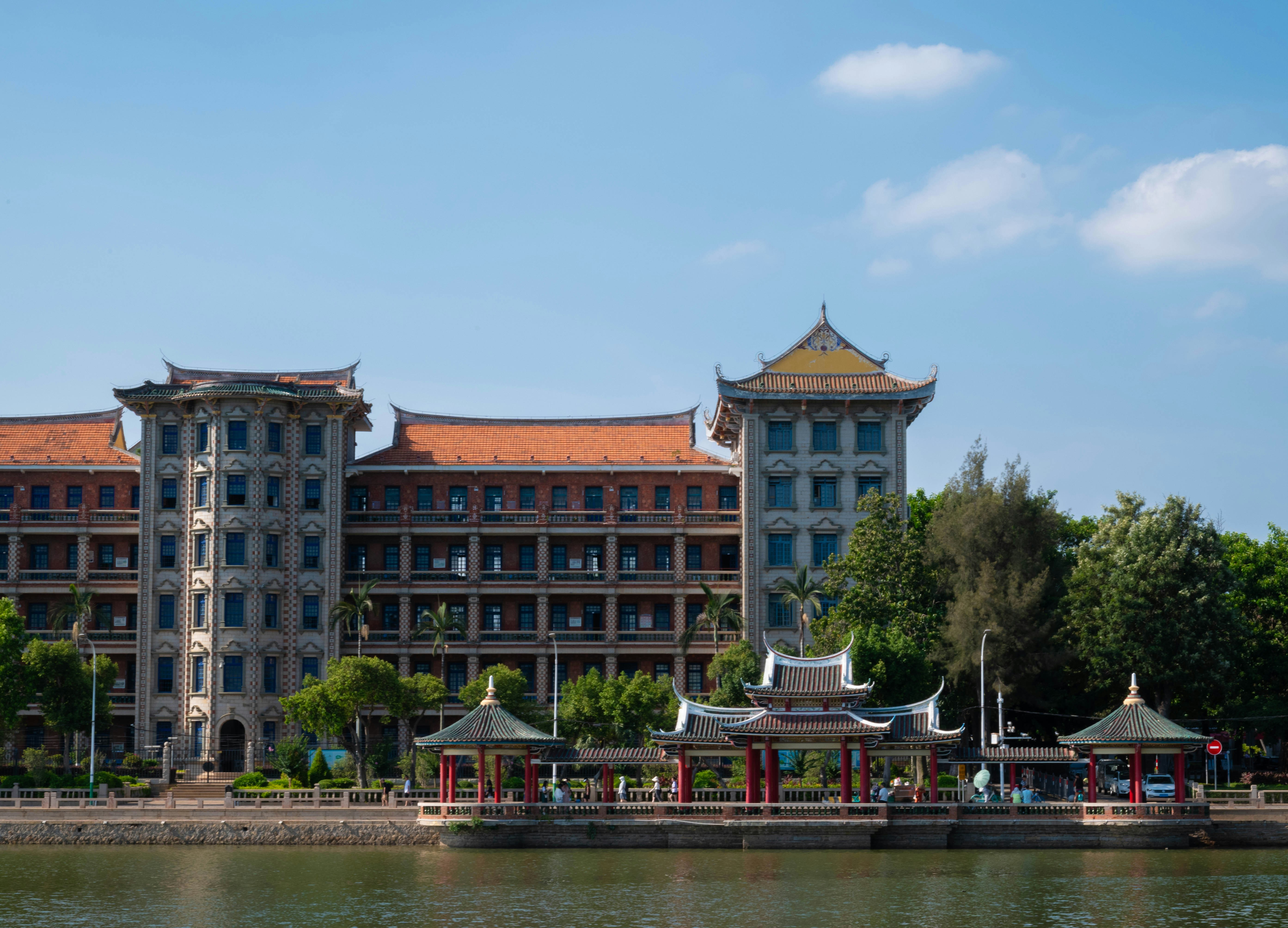 Traditional Chinese buildings with curved roofs by a serene lakeside under a clear blue sky.