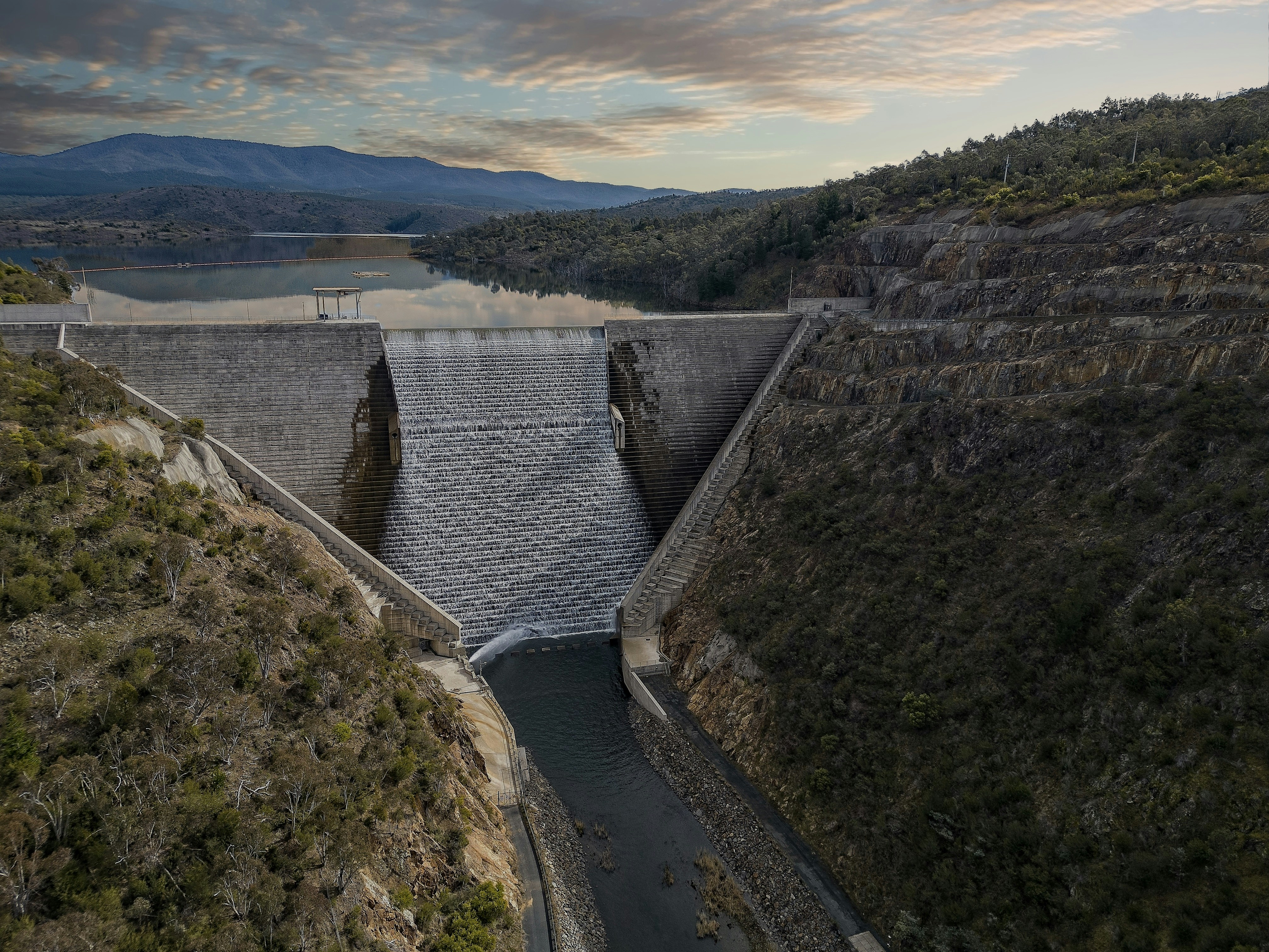 An aerial view of a dam with a lake and mountains in the background ...