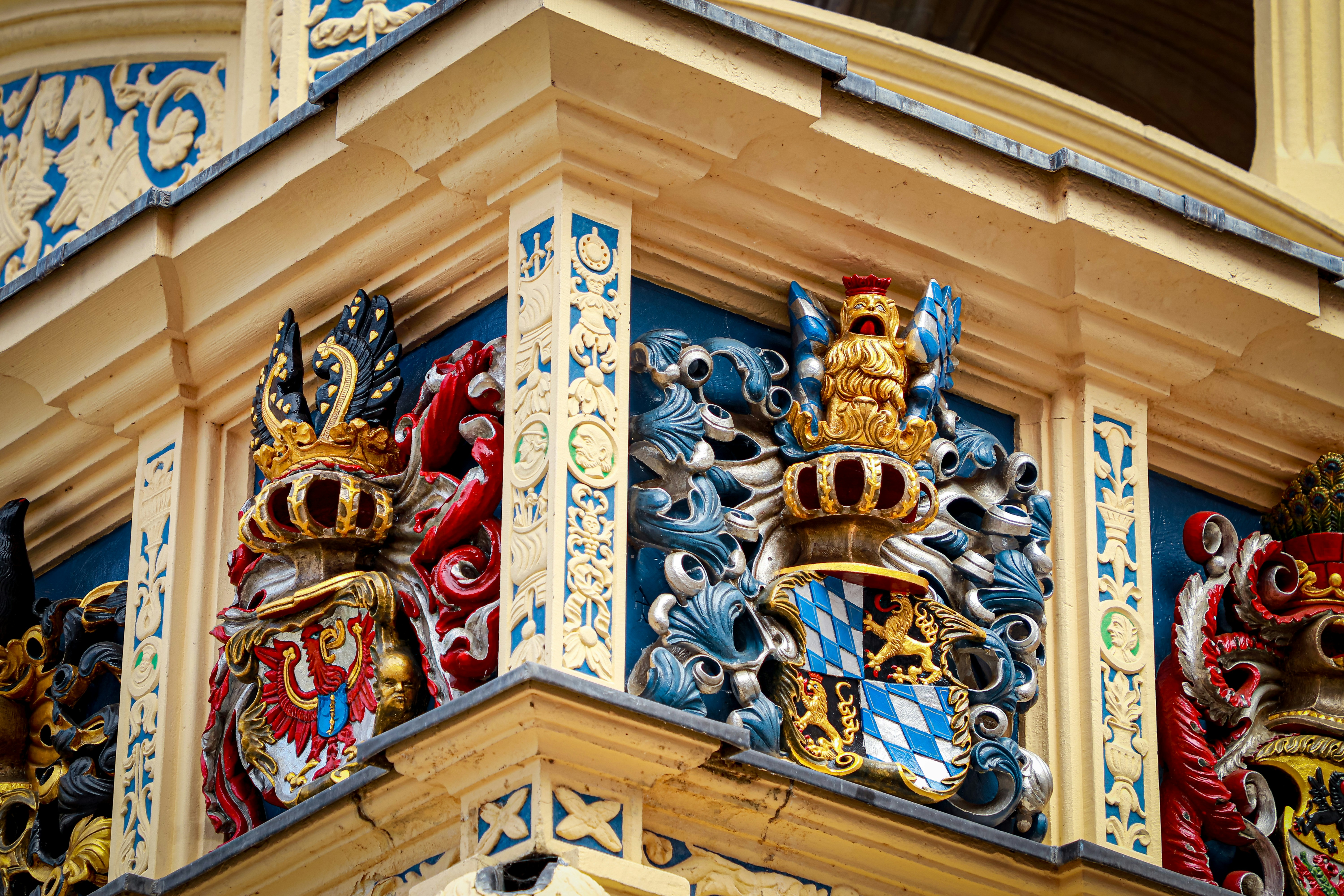 Ornate heraldic carvings with vibrant crests and crowns on a building facade.