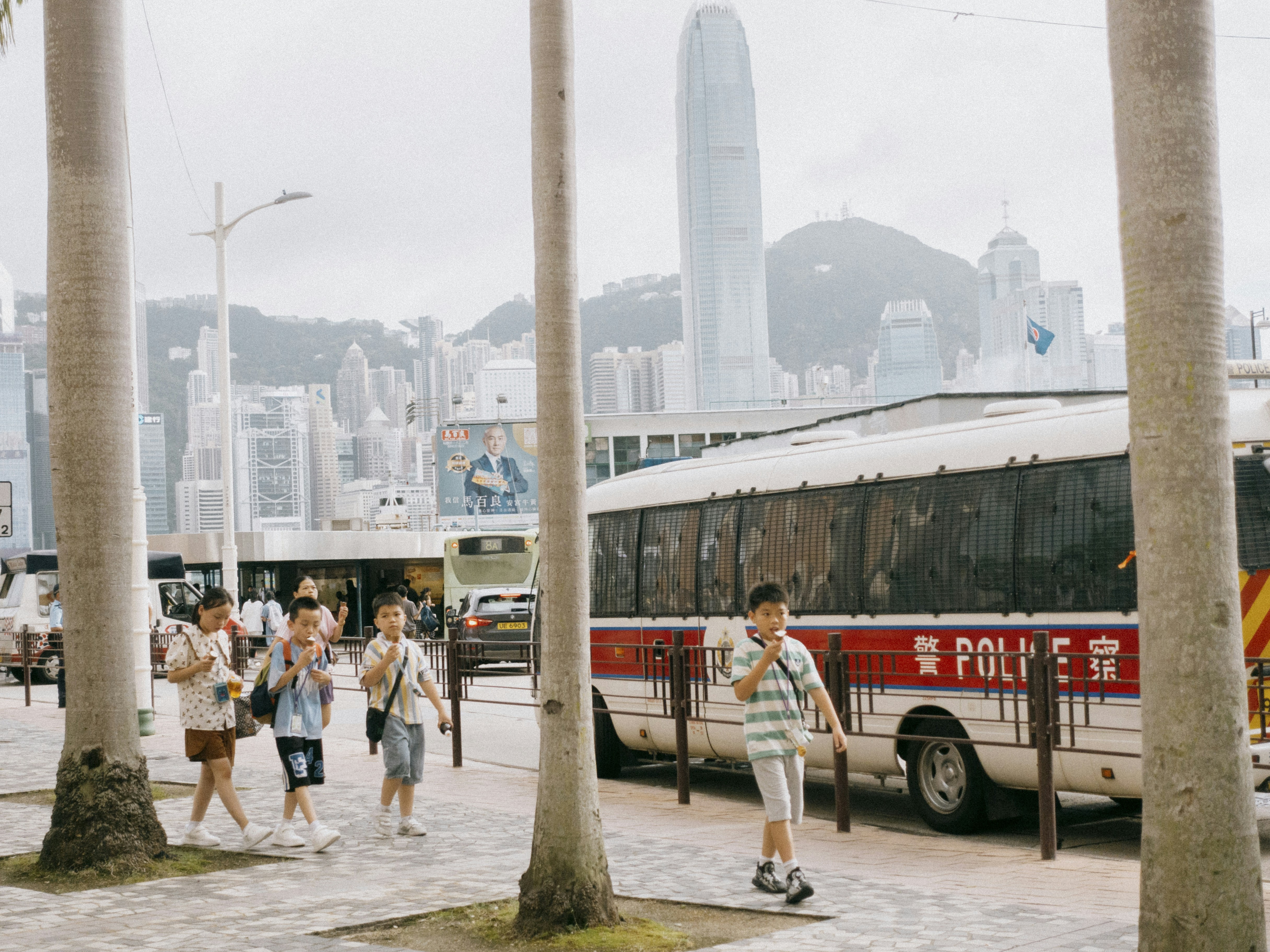 Waterfront Walk: Children Near a Police Bus with a Distant Skyline