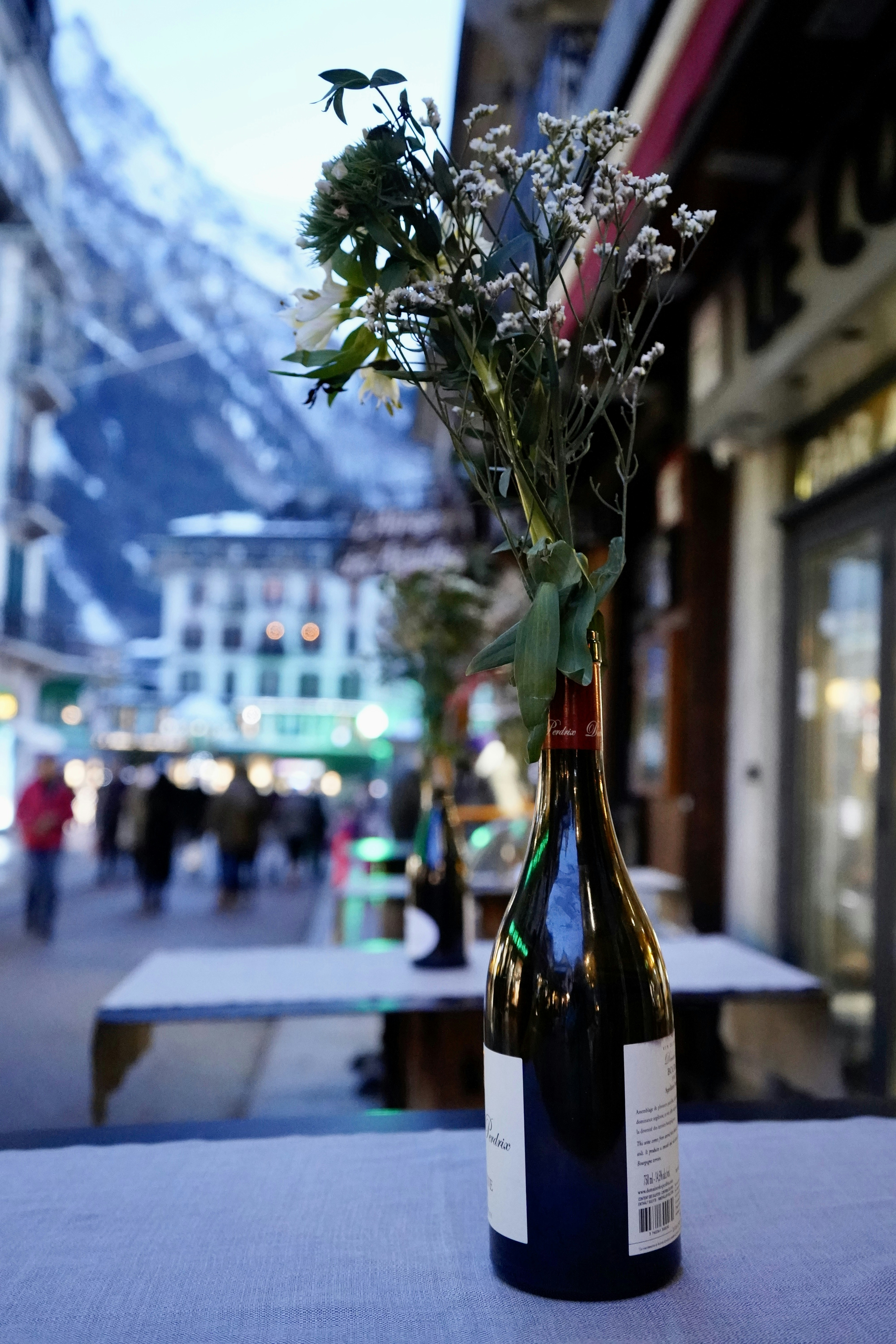 Floral Bottle on a Café Table Framed by Neon Street Blur