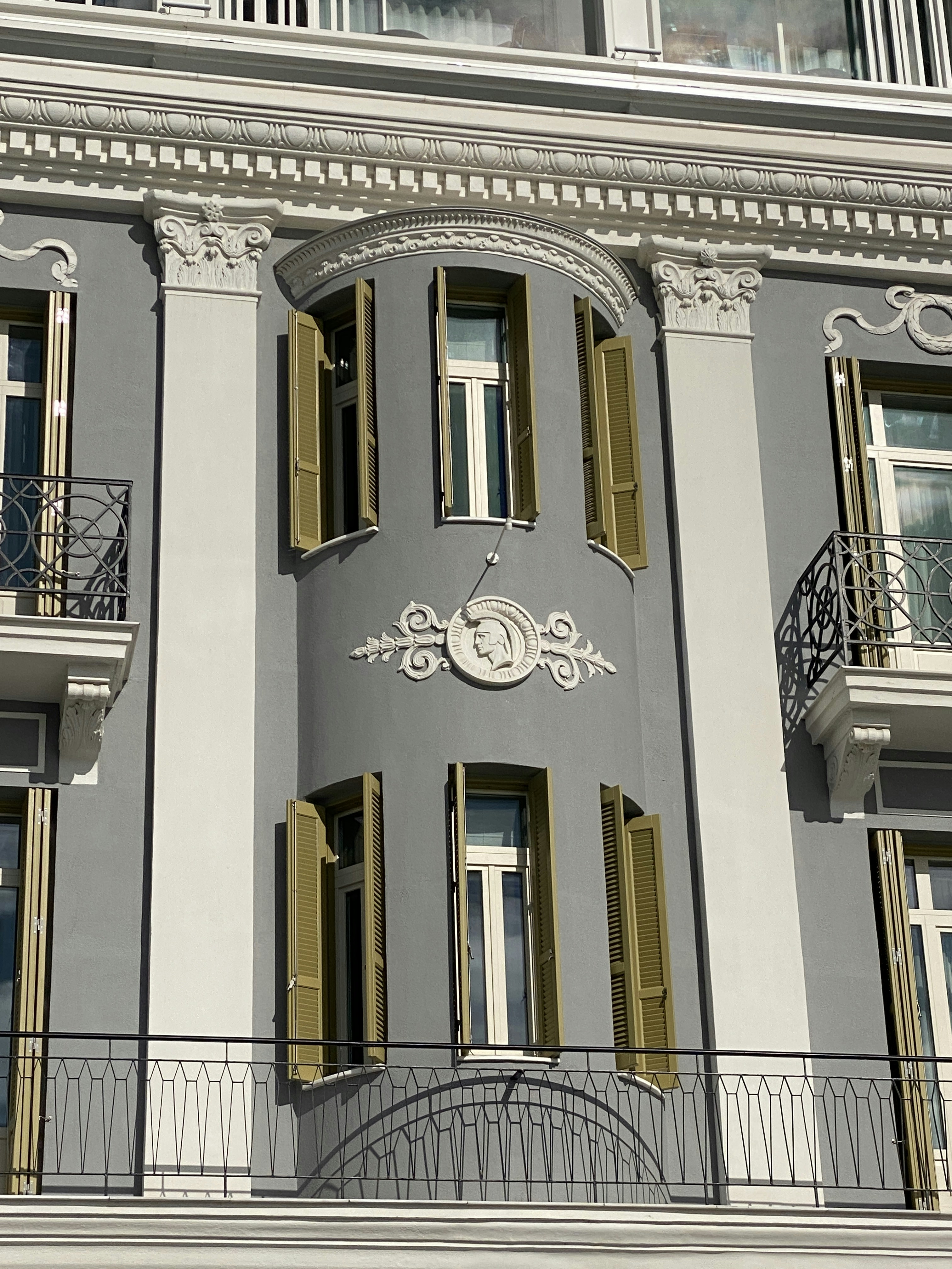 Heraldic Crest Framing a Curved Window on a Gray Classical Facade