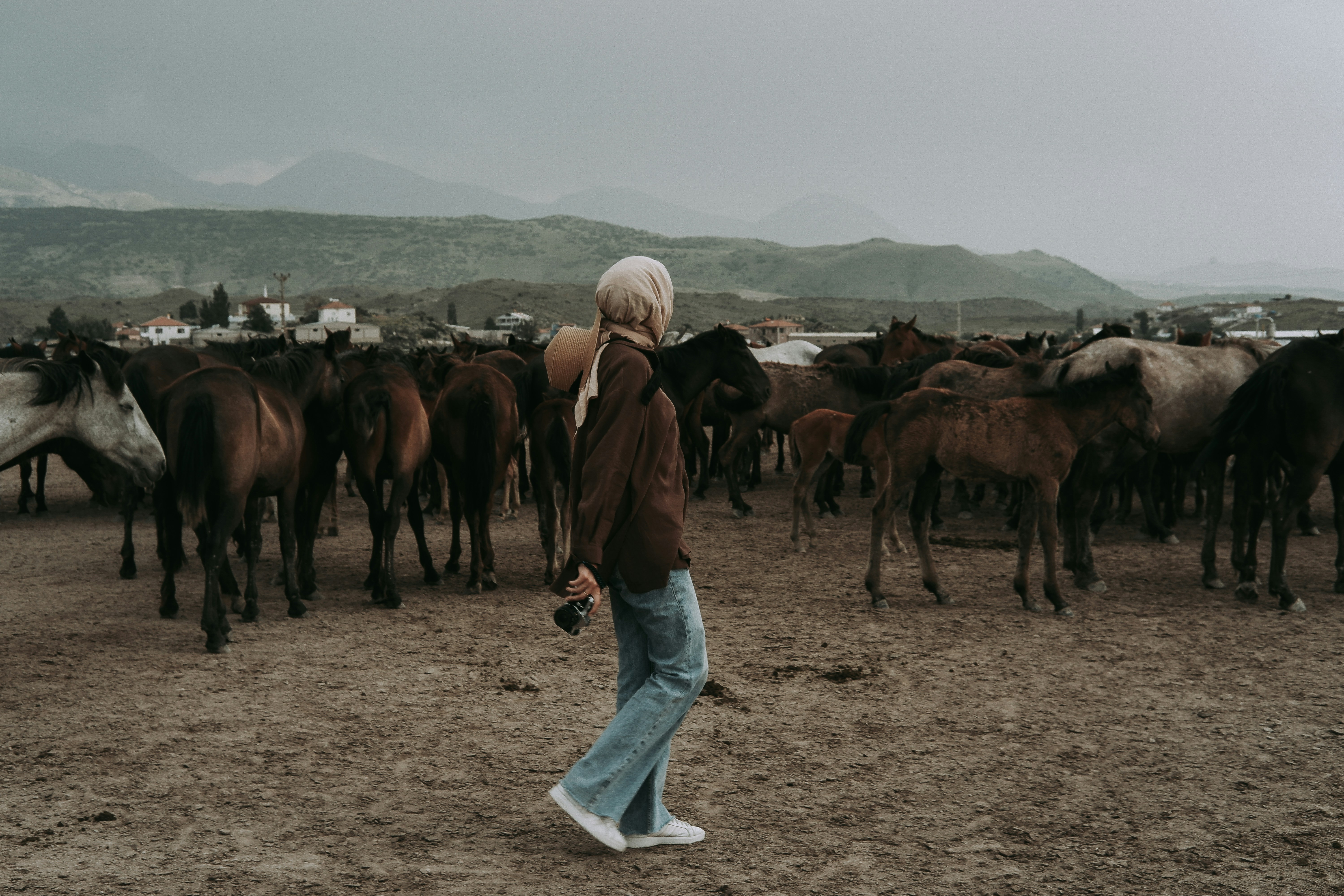 a woman walking in front of a herd of horses