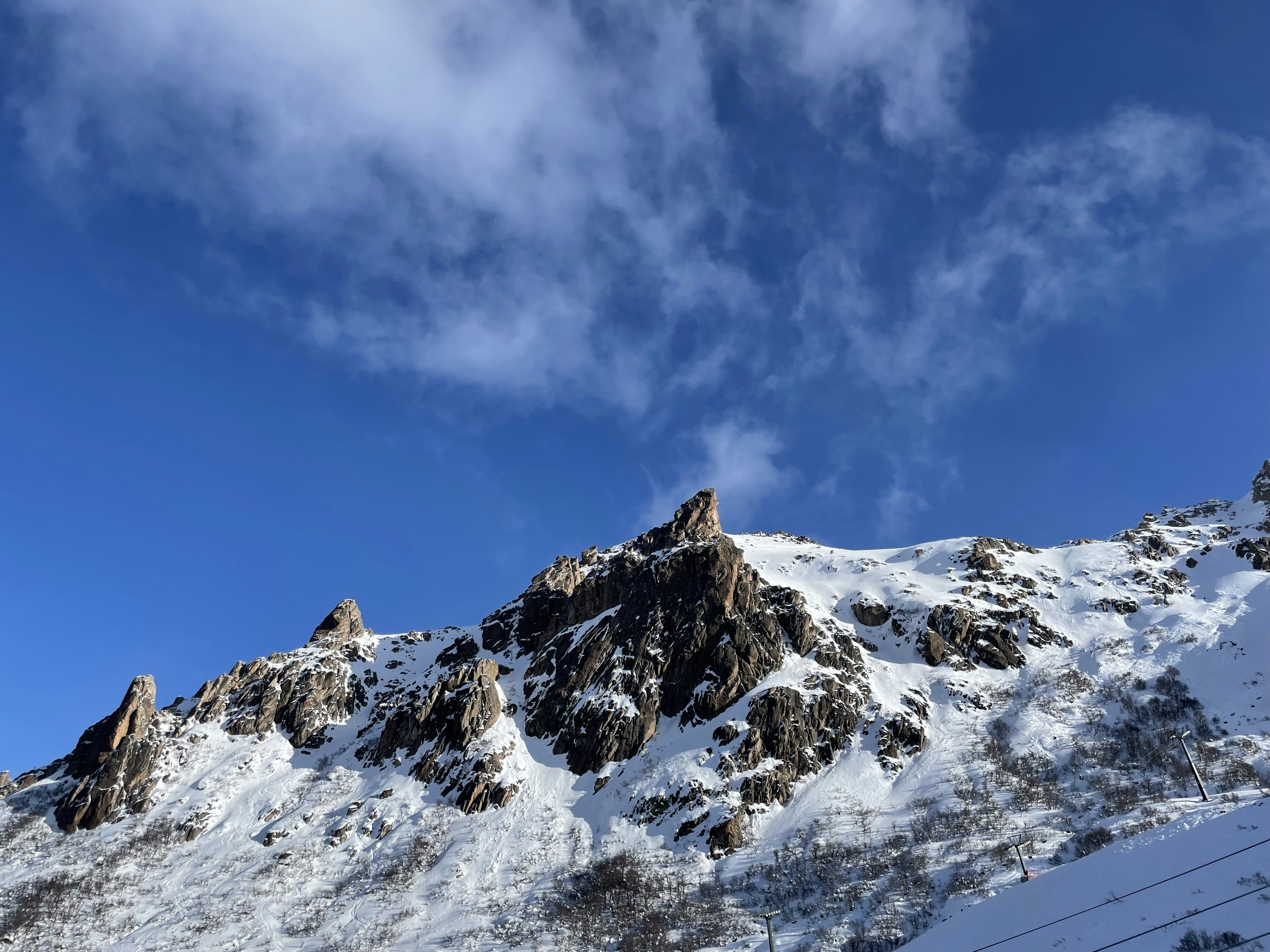 Snow-covered mountain with rugged rocky outcrops under a clear blue sky.