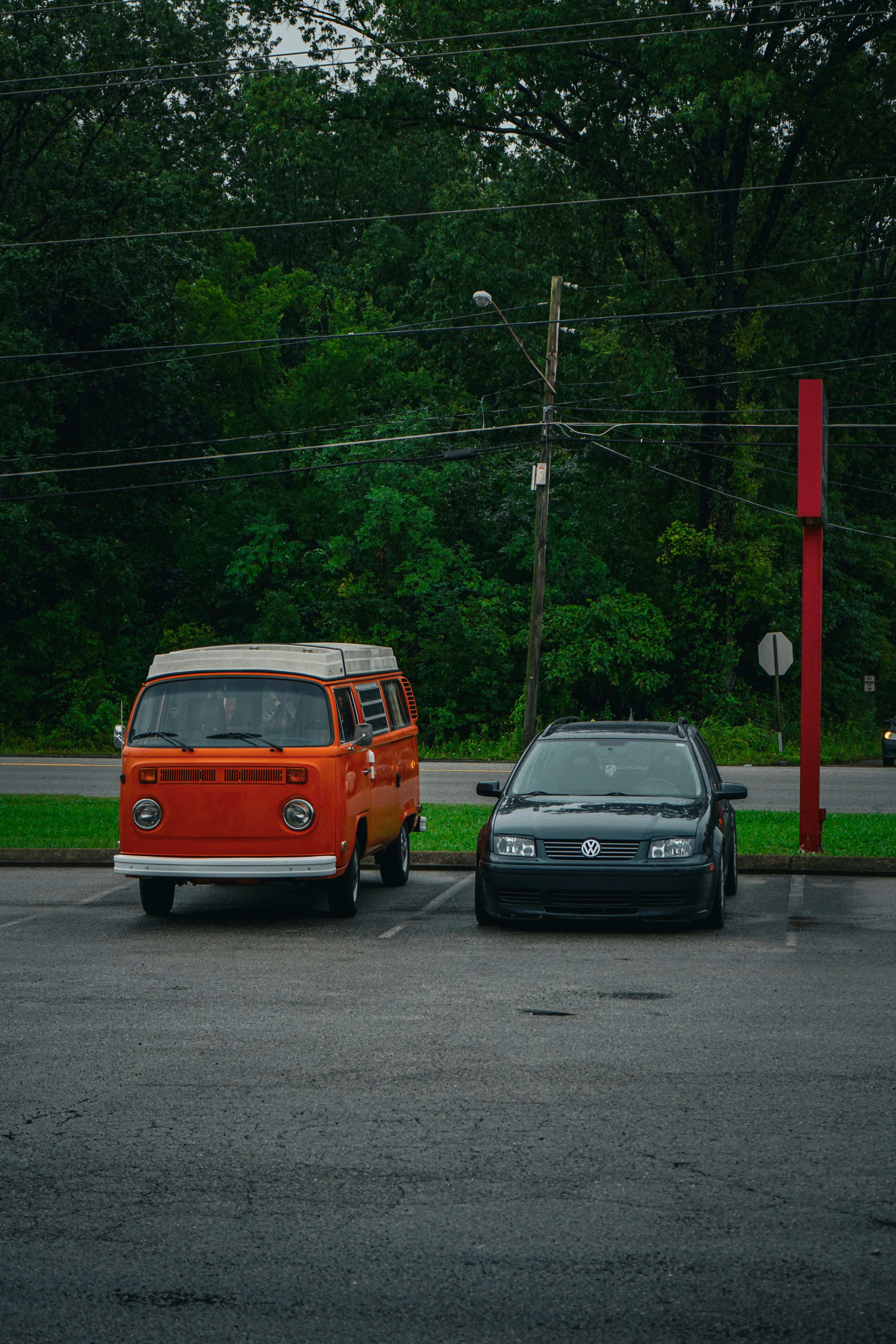 Orange VW Microbus and a Modern Sedan: Quiet Clash in a Rain-Worn Parking Lot
