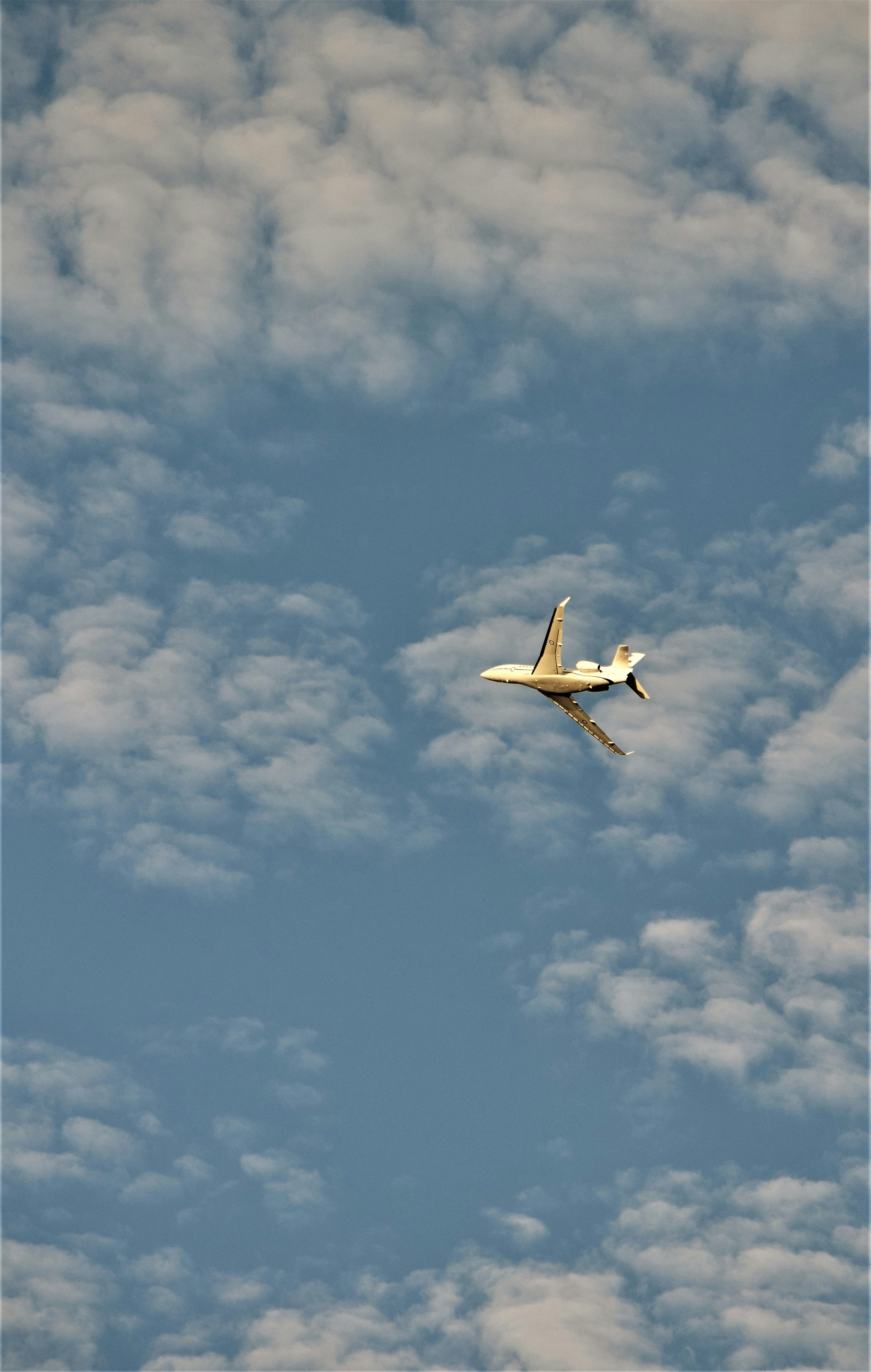 A sleek aircraft maneuvers gracefully against a backdrop of fluffy clouds and clear blue sky.