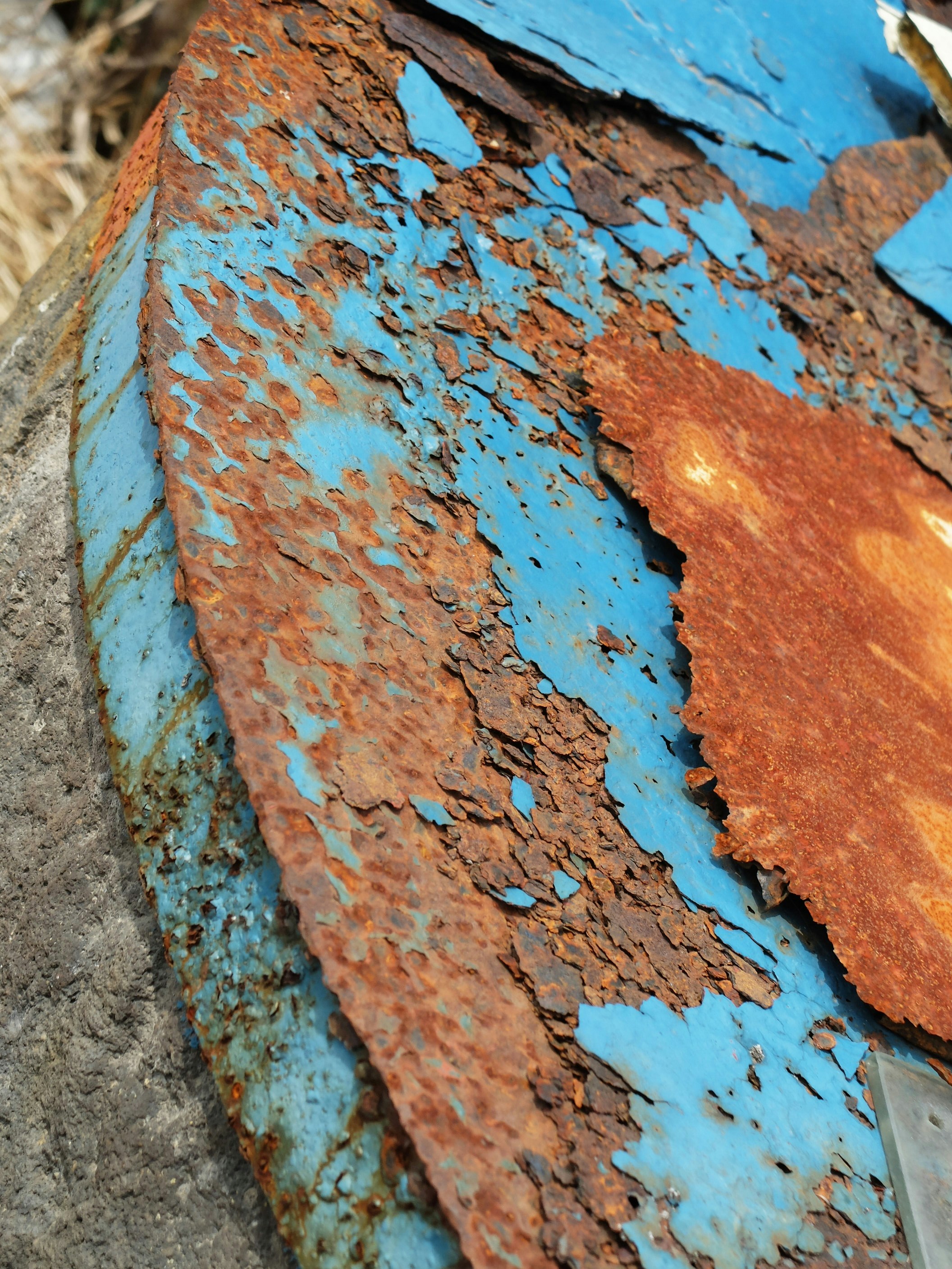 Close-up of peeling turquoise paint on rusted metal, revealing textured layers and patina.