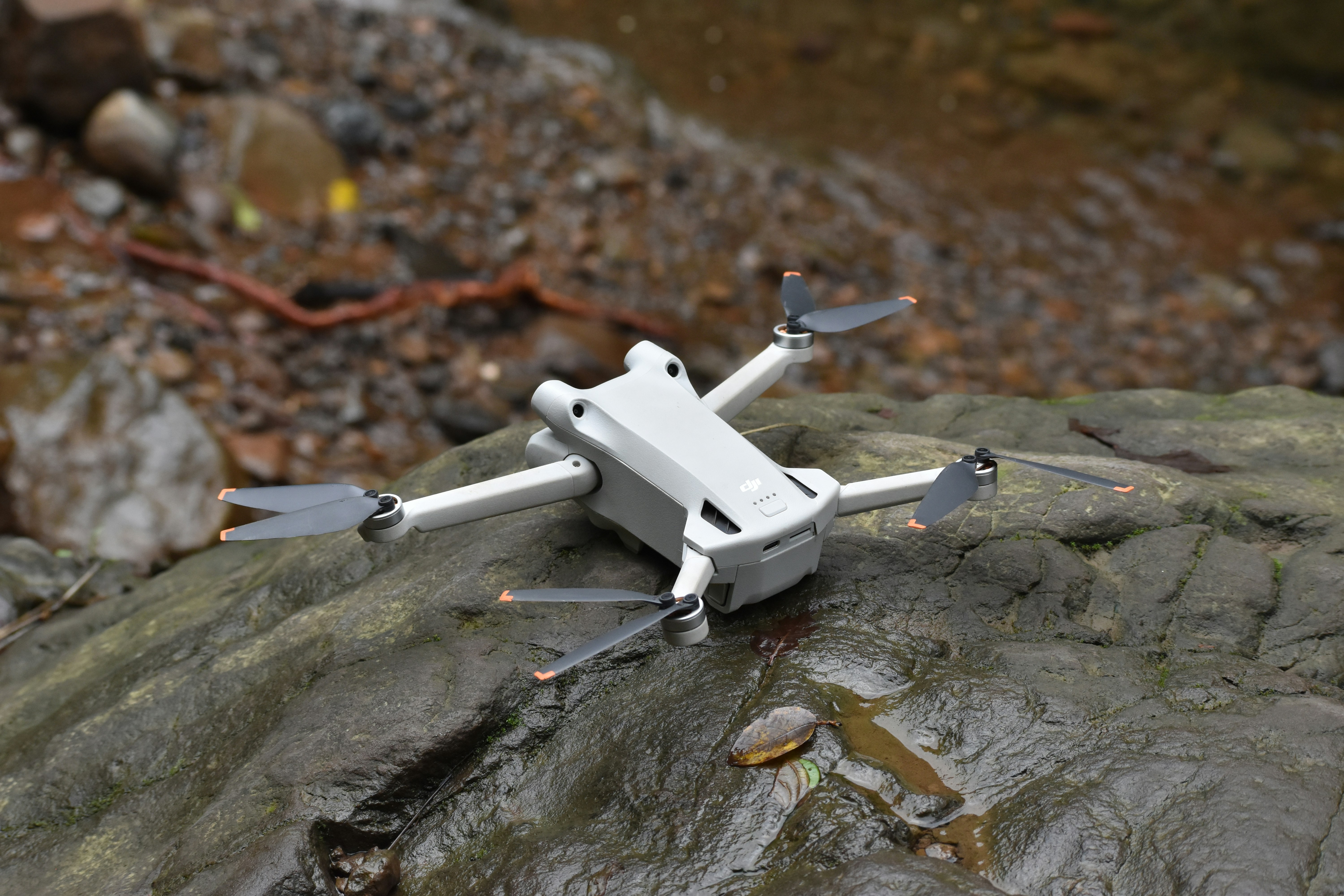 Rain-Wetted Granite Perch: A White Quadcopter by the Creek