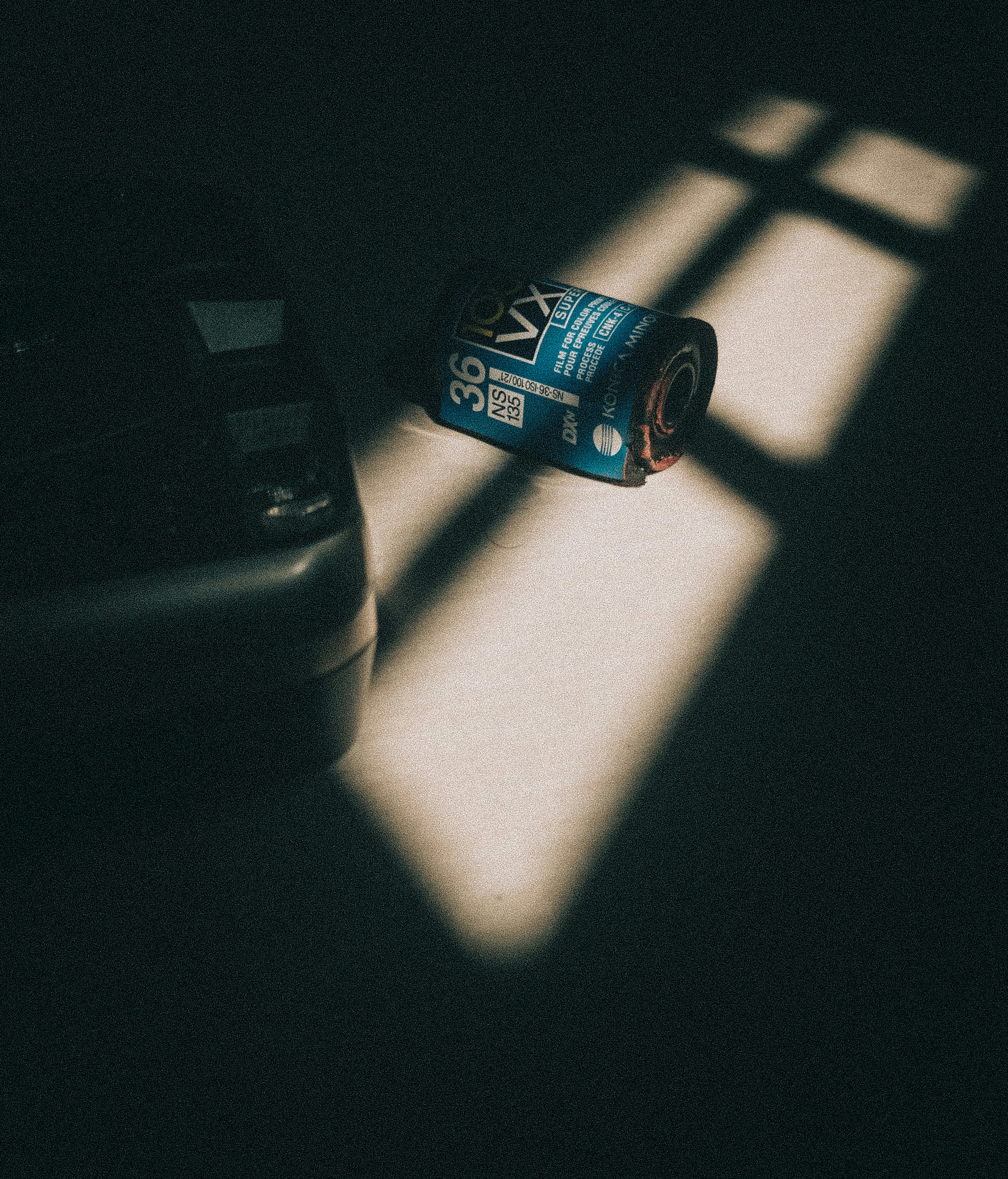 Photograph of a blue AA-sized battery resting on a dark surface, with diagonal light stripes from window blinds crossing it.