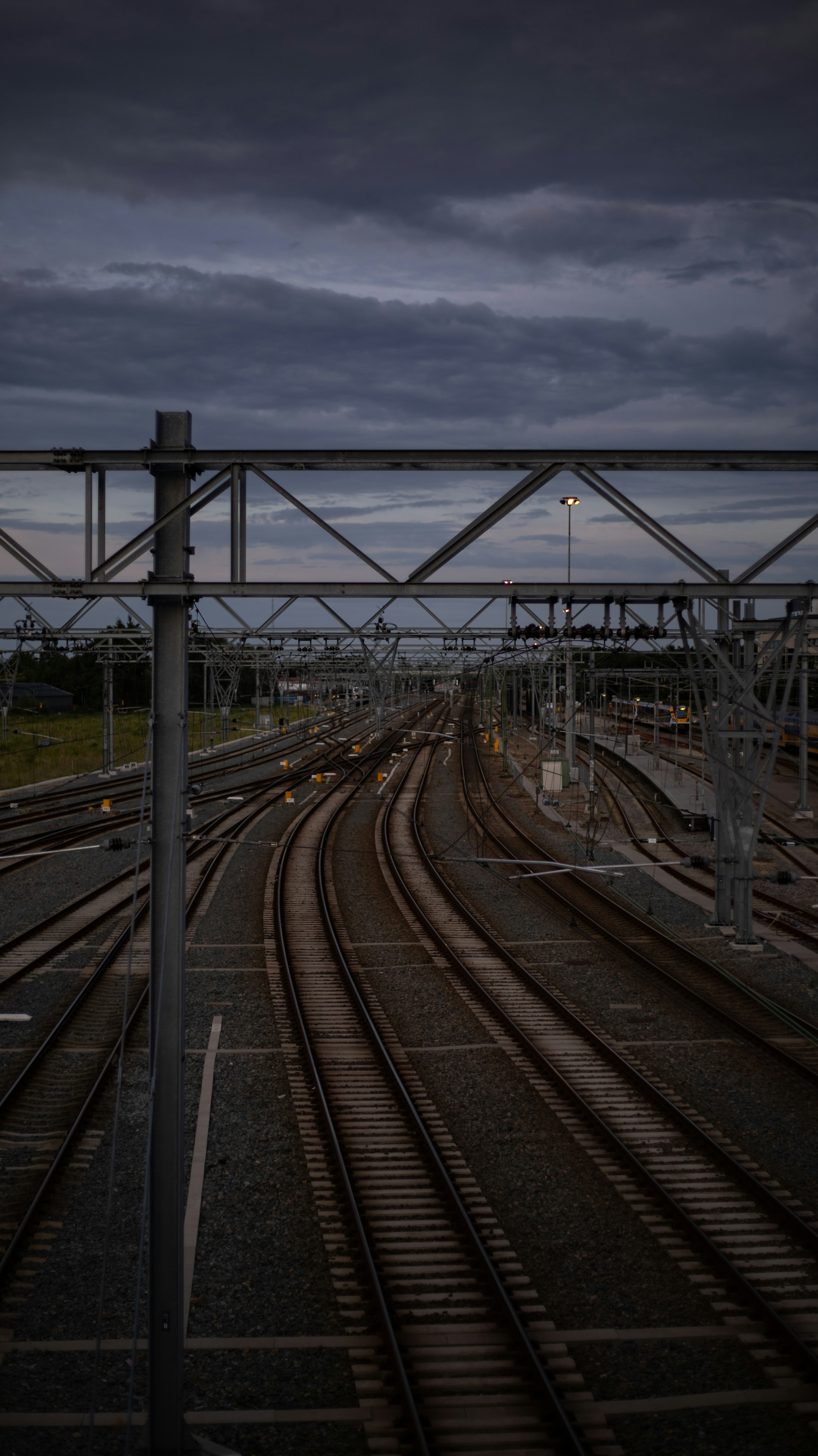 Railway tracks curving into the distance under a moody sky, illuminated by overhead lights. The scene conveys a sense of quiet anticipation and industrial elegance.