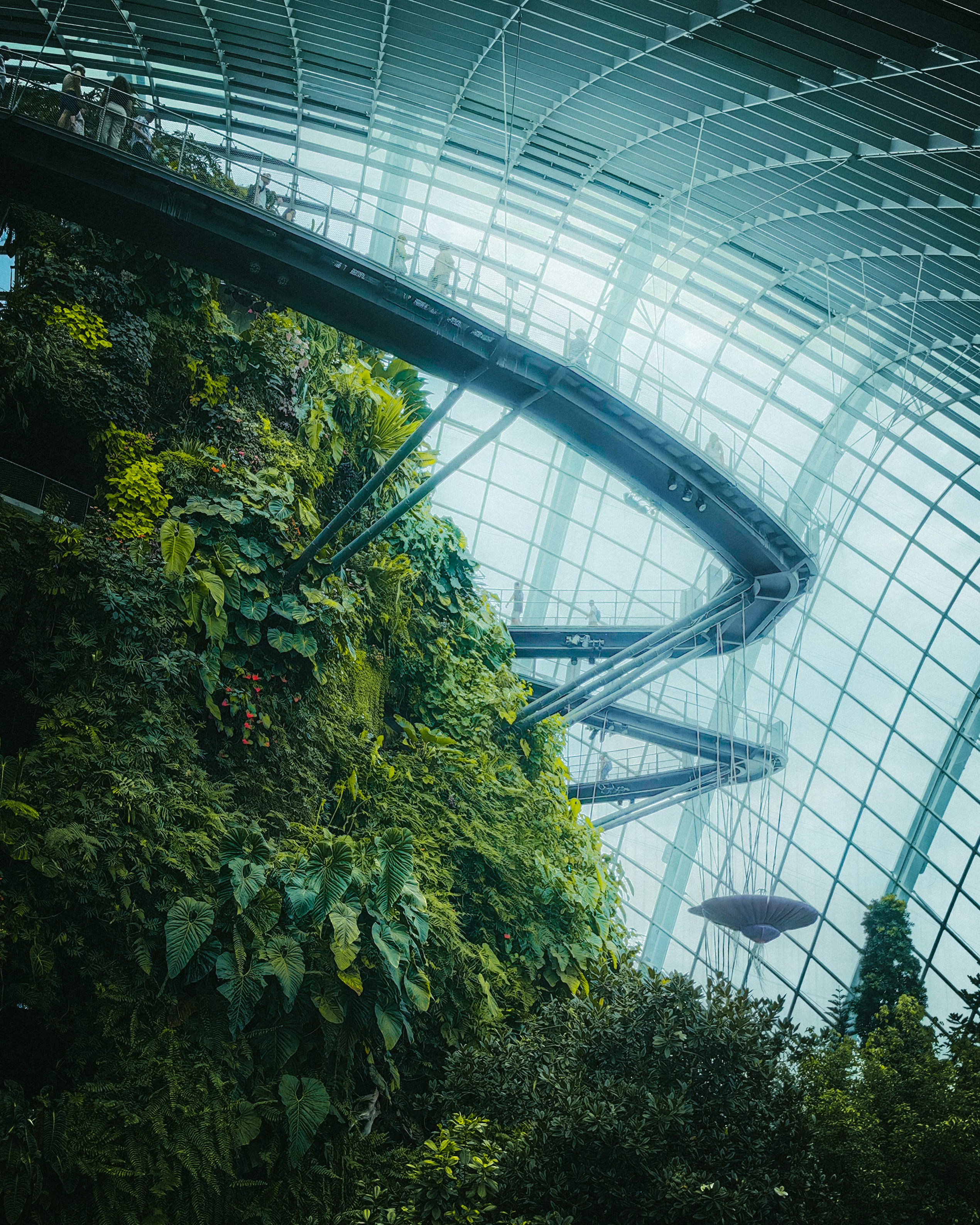 Lush green wall climbs beside a curved glass-and-steel atrium, bathed in cool blue light.